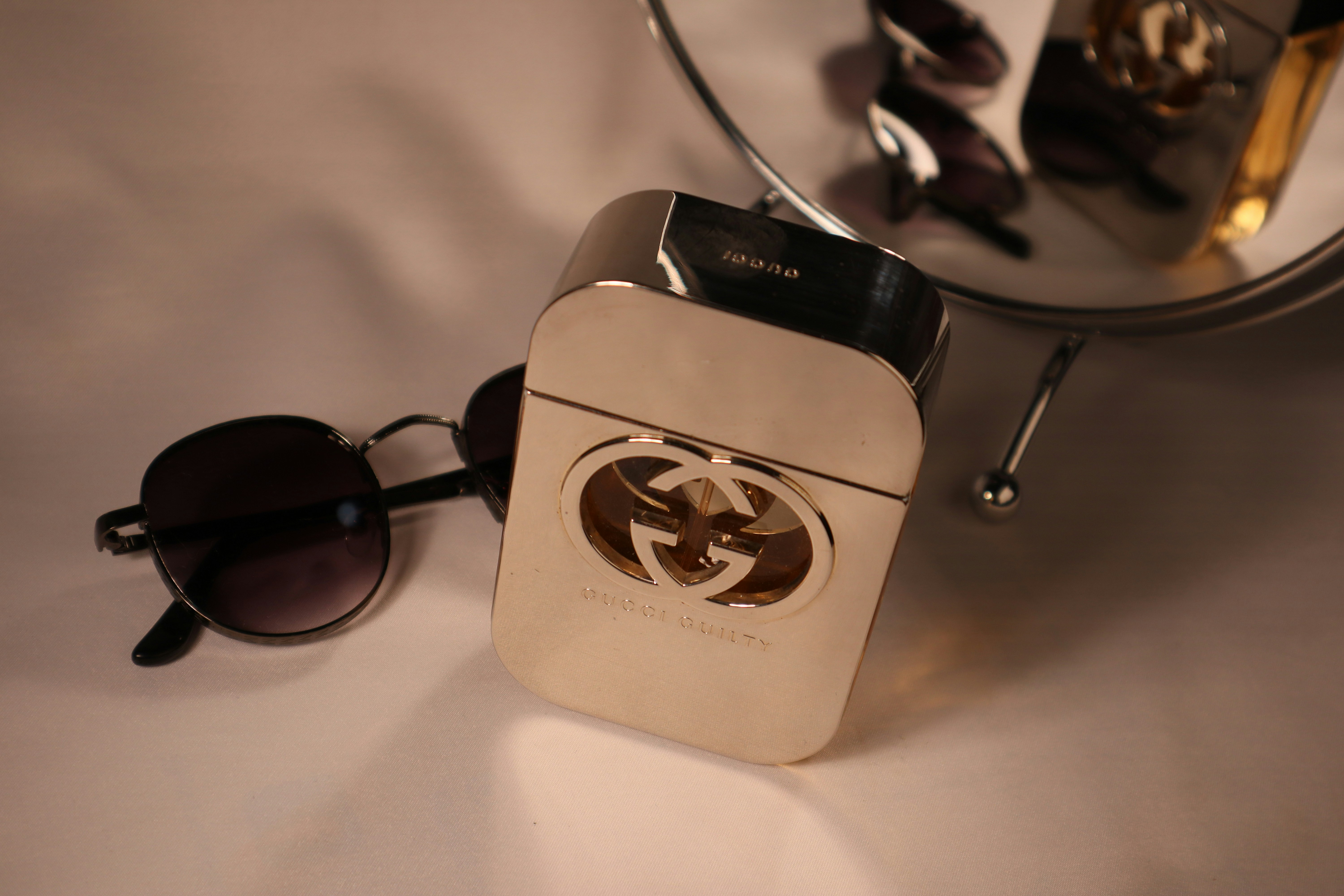 Gucci Guilty Eau de Toilette Pour Femme features a unique ambery floral accord, blending lilac petals with citrus, amber notes, and patchouli for a fresh, feminine scent. https://fashionneedles.in/product-category/luxury-perfume/ | Gucci perfume, sunglasses, and accessories are on display.