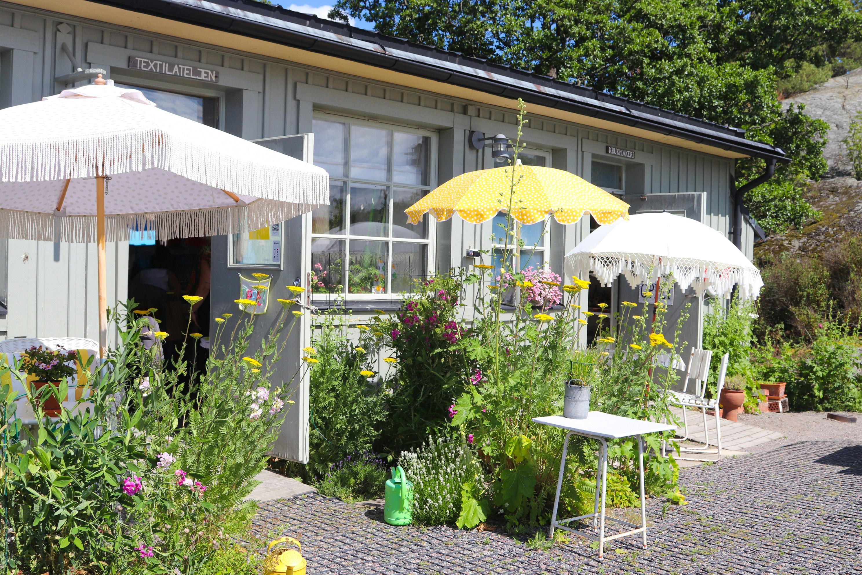 Charming outdoor scene featuring colorful umbrellas and lush flowers surrounding a quaint building. Ideal for leisurely afternoons.
