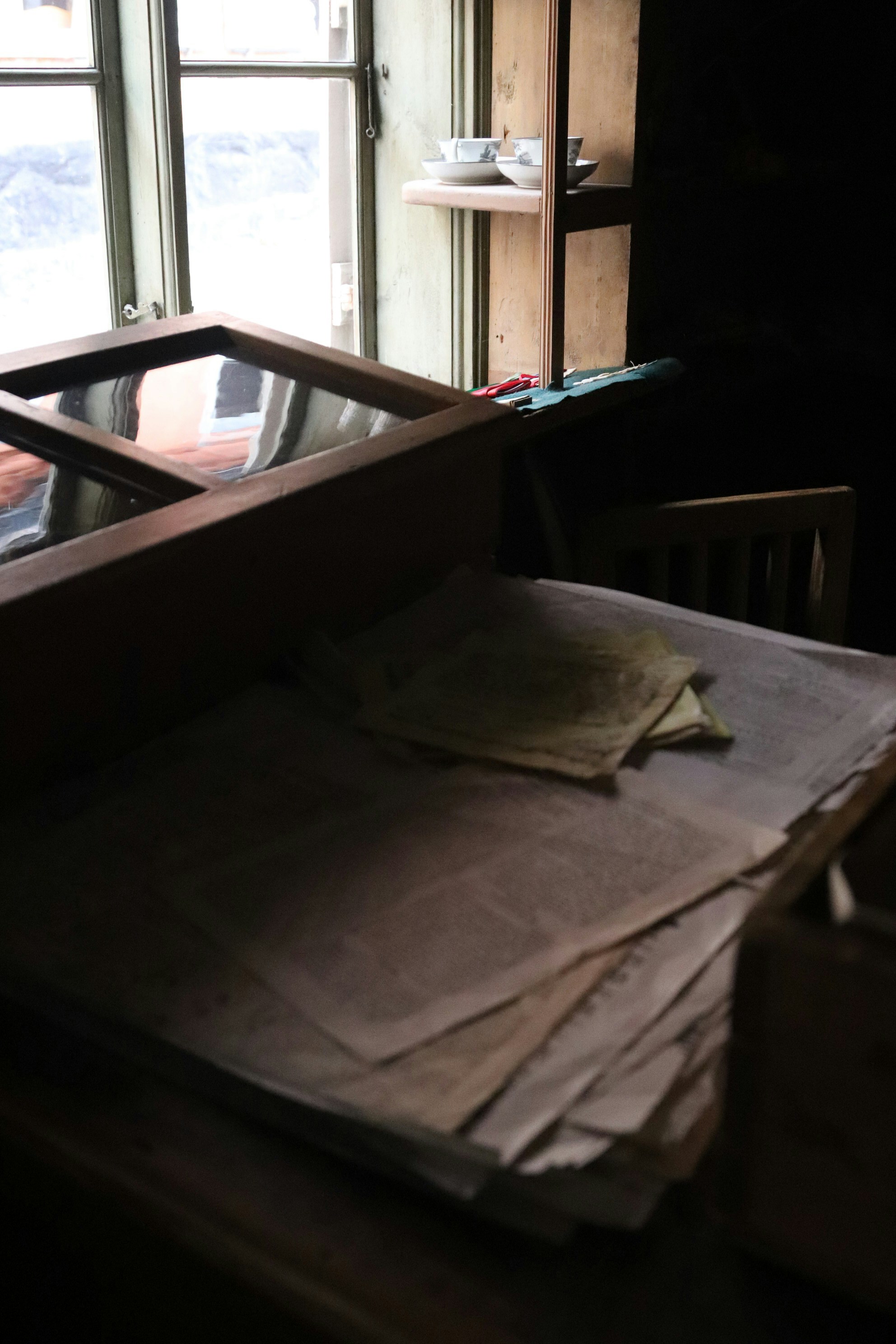 Old papers scattered on a wooden table, illuminated by soft light from a nearby window, creating a nostalgic atmosphere.