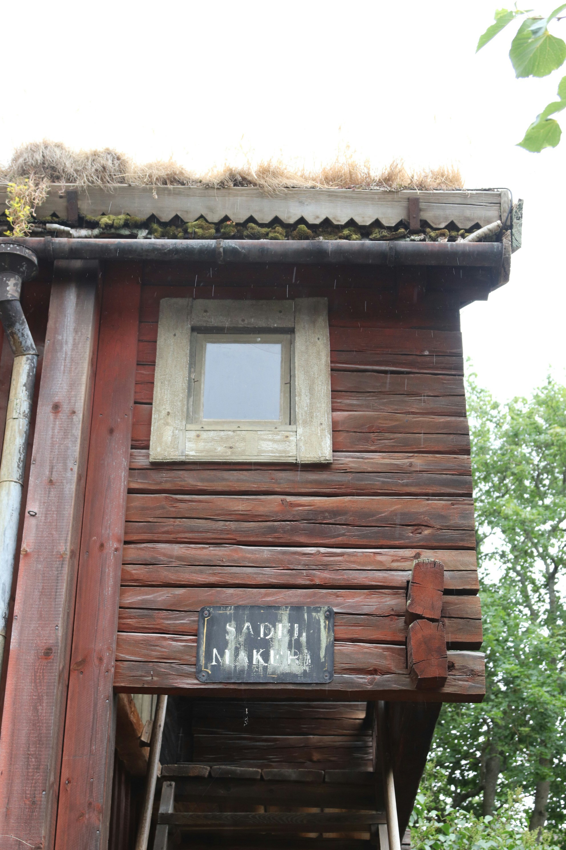A red wooden building has a grass roof.