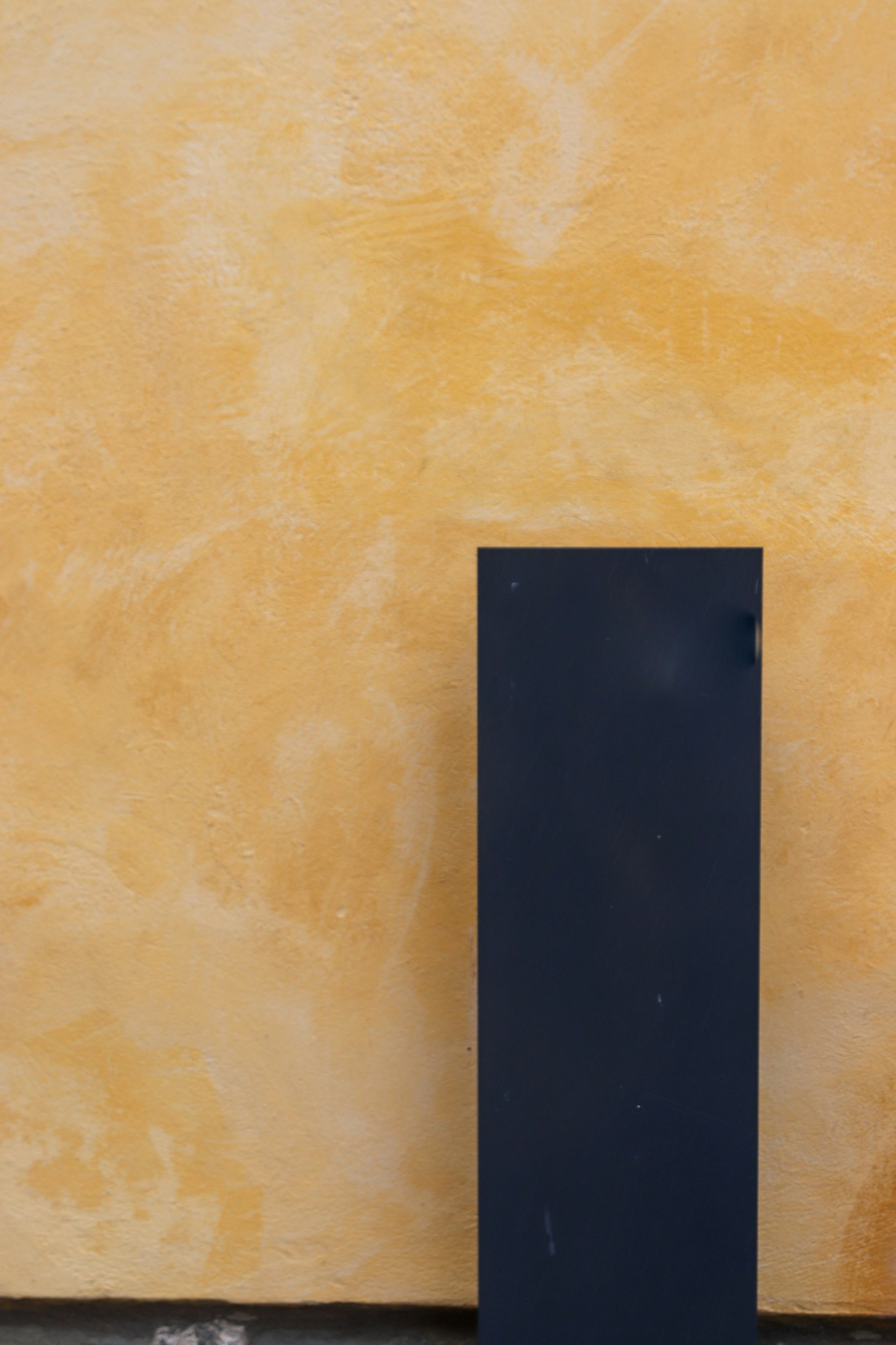 A dark rectangular object is in front of yellow wall.