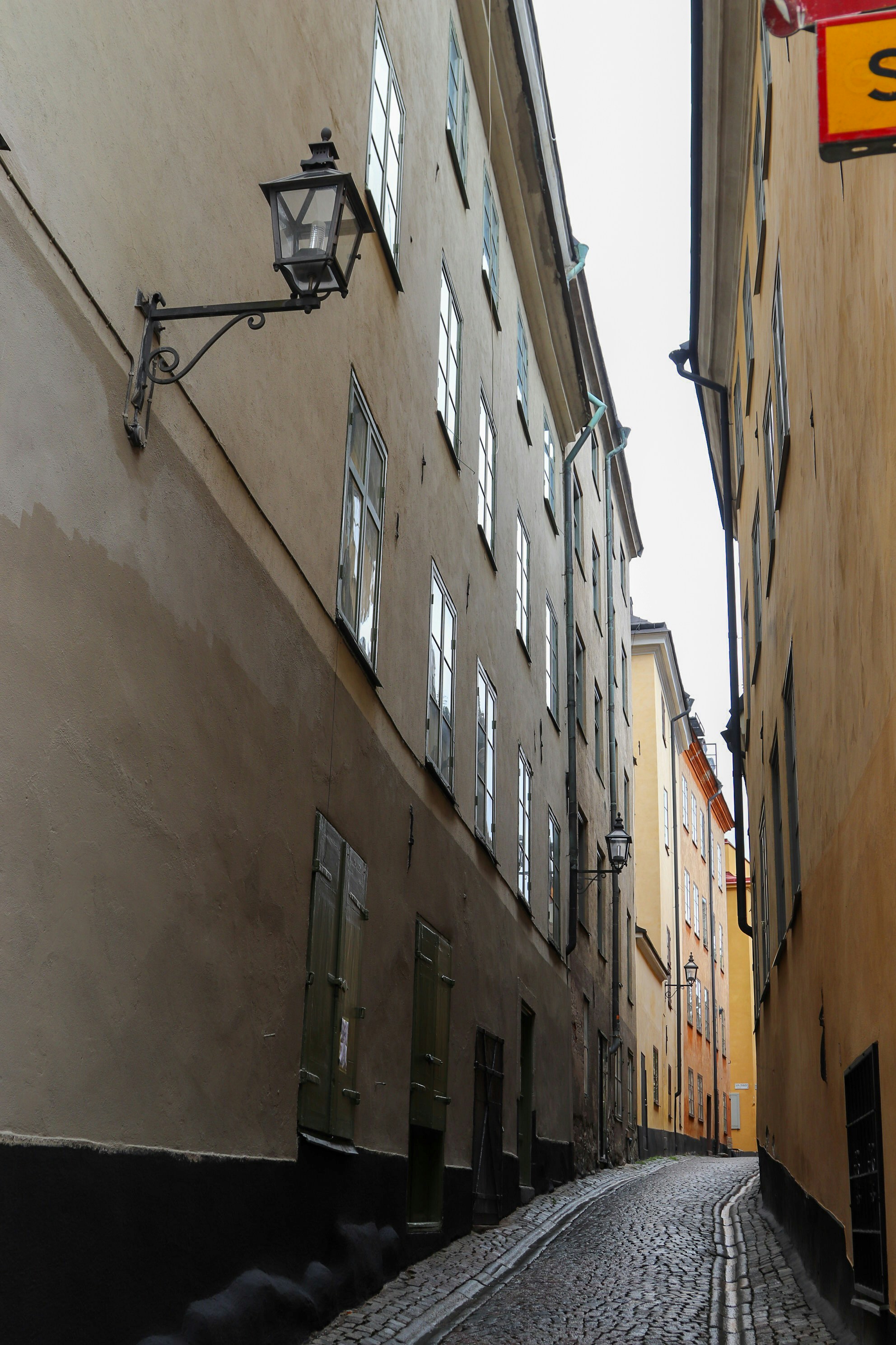 Charming cobblestone street flanked by tall, colorful buildings under a gray sky. Vintage lanterns add a touch of nostalgia.
