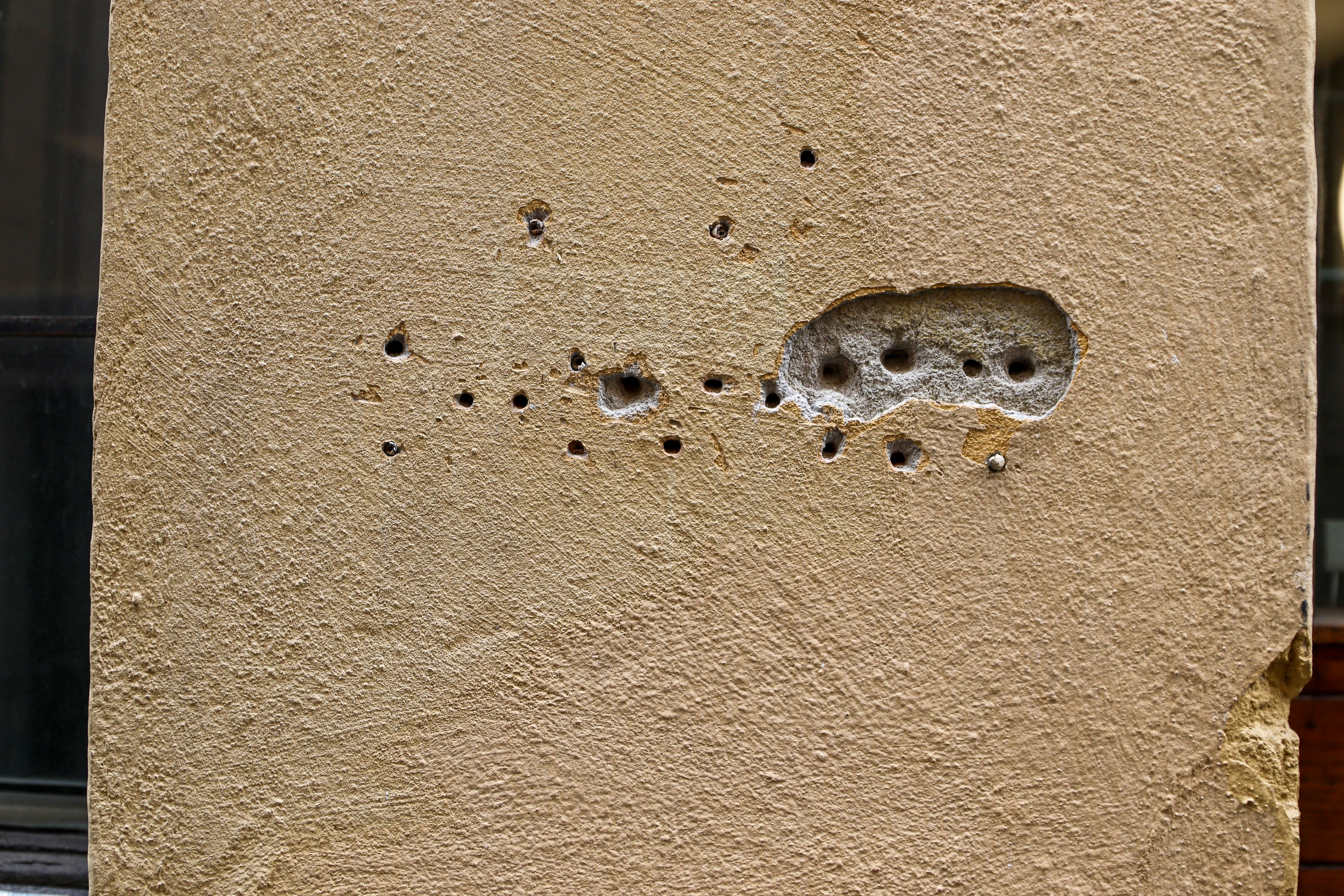Scarred Facade: A sunlit stucco wall punctured by a dense cluster of holes