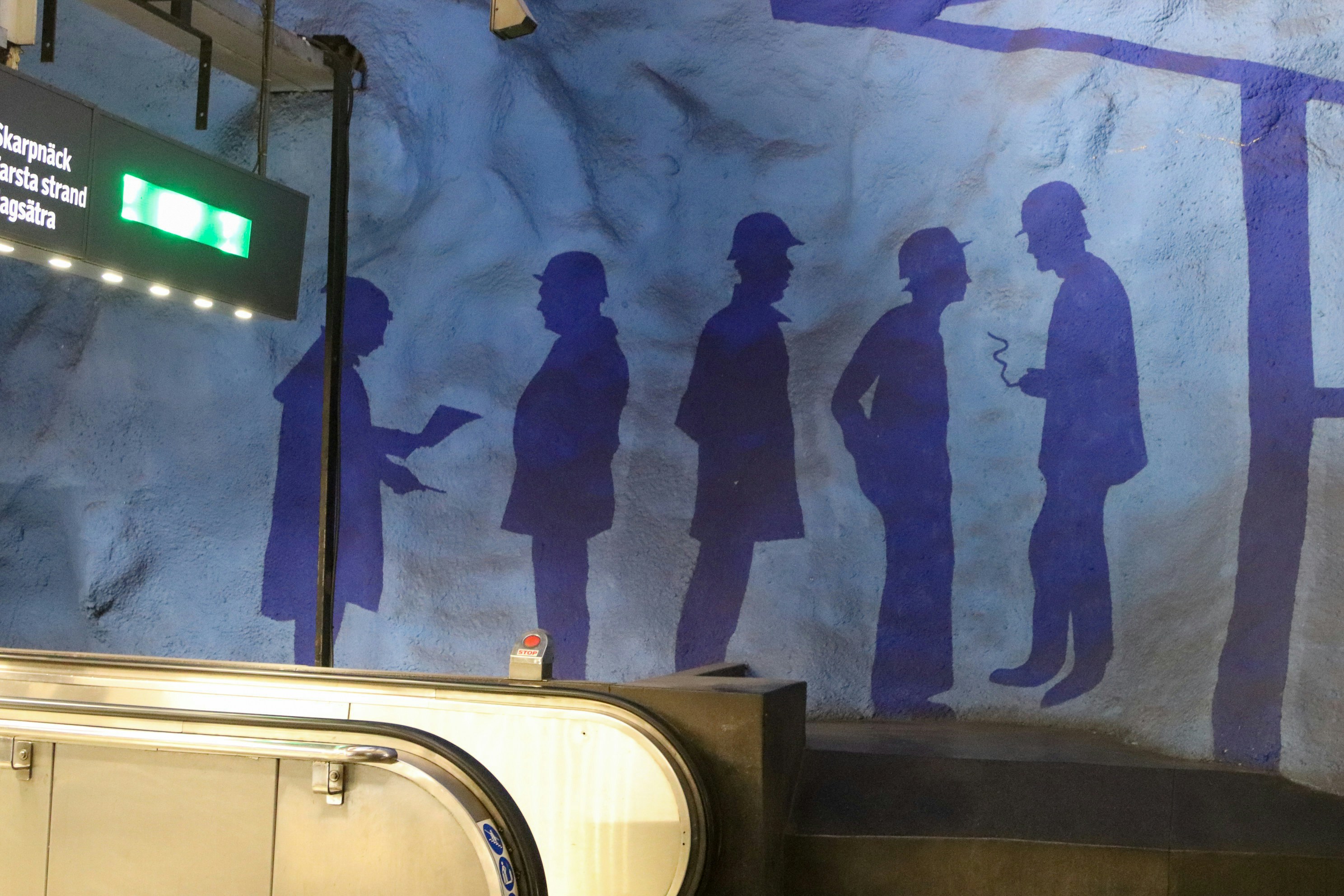 Silhouetted figures cast against a textured wall in a subway station, depicting a moment of urban life. The scene evokes a sense of connection among commuters.