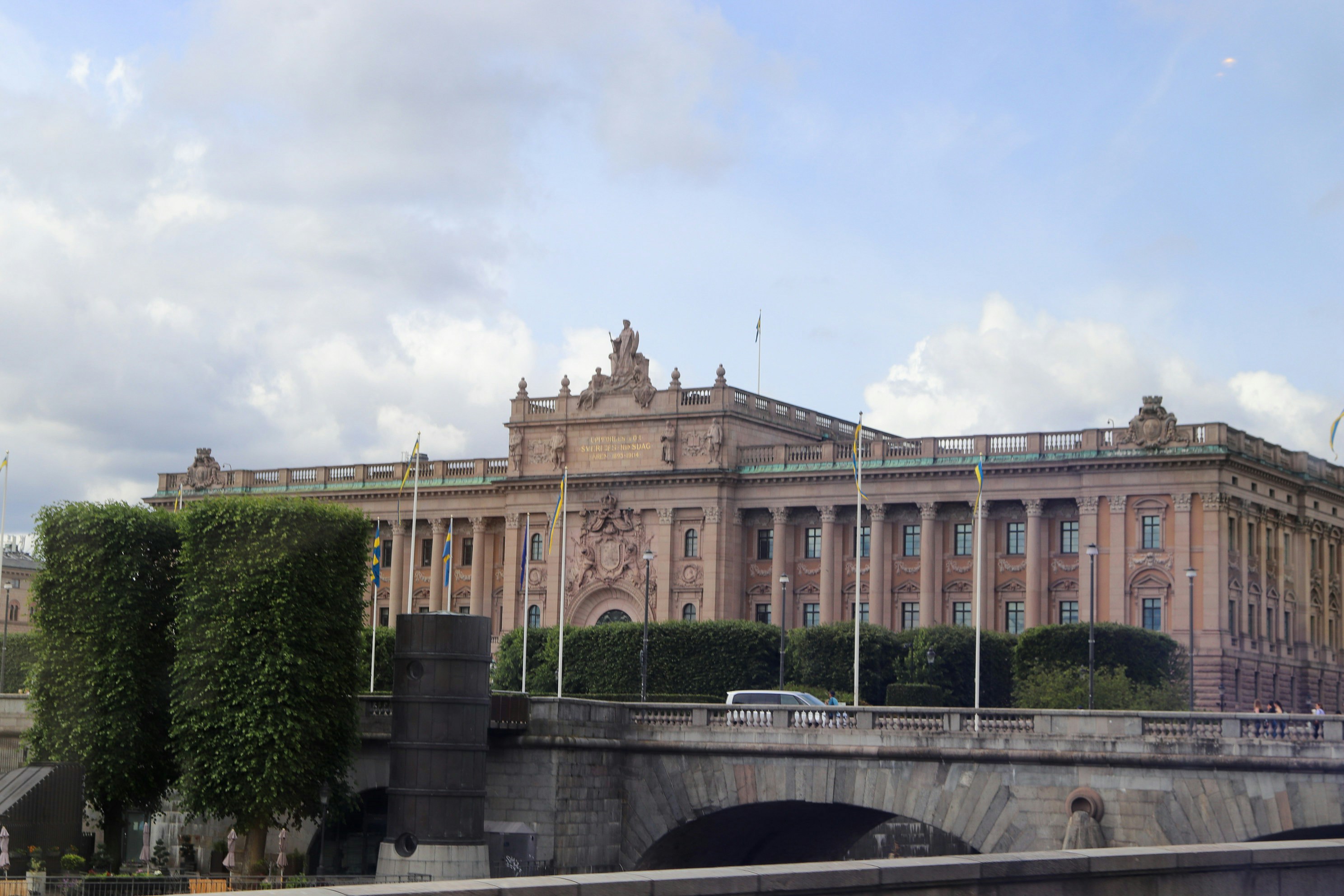 Sweden's Parliament building framed by lush greenery and a tranquil waterway, showcasing its historical architecture and grandeur.