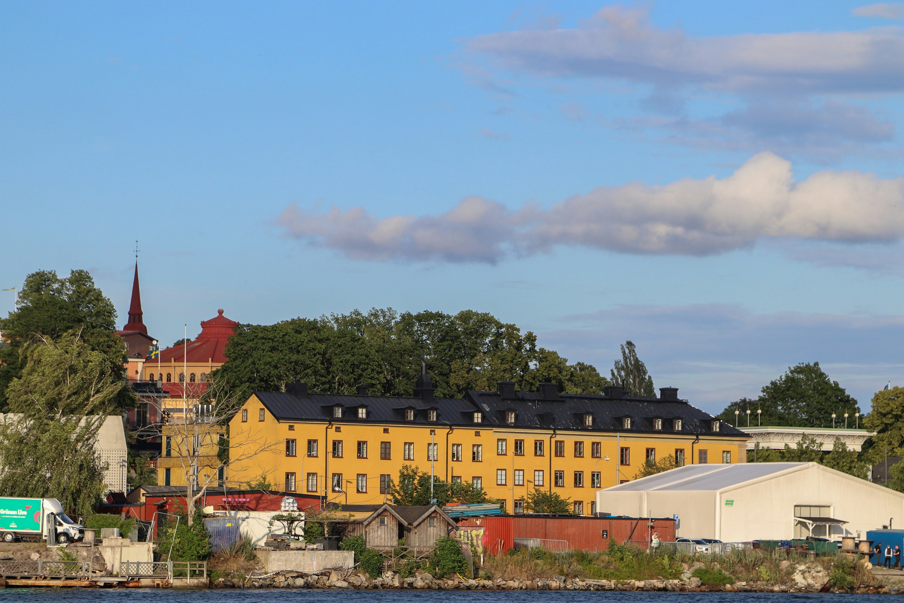 Historic buildings nestled among greenery along the waterfront, showcasing a blend of architecture and nature.
