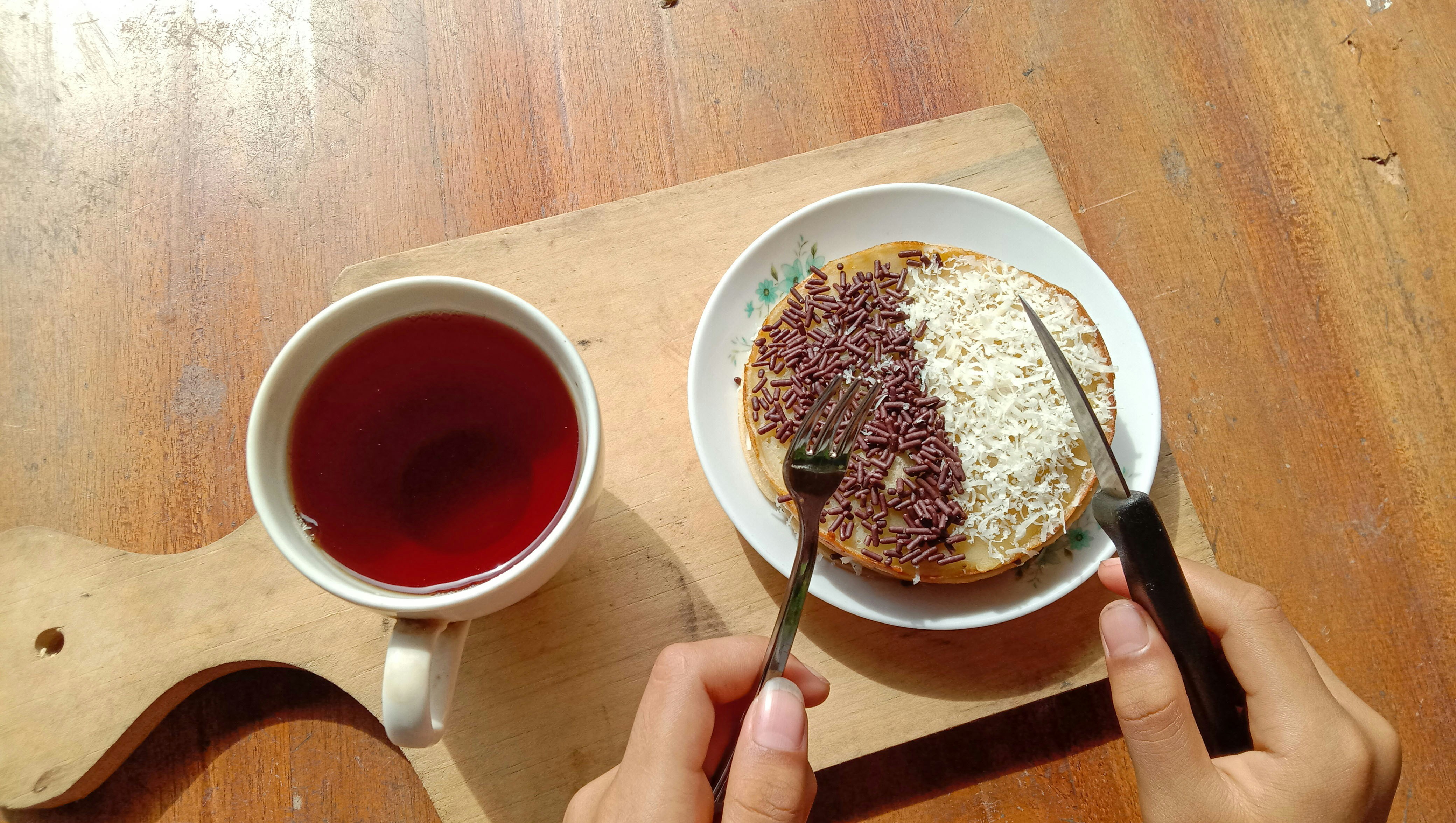 A photo of someone eating a mini martabak and drinking a cup of tea on a wooden table | Breakfast of tea and pancake.
