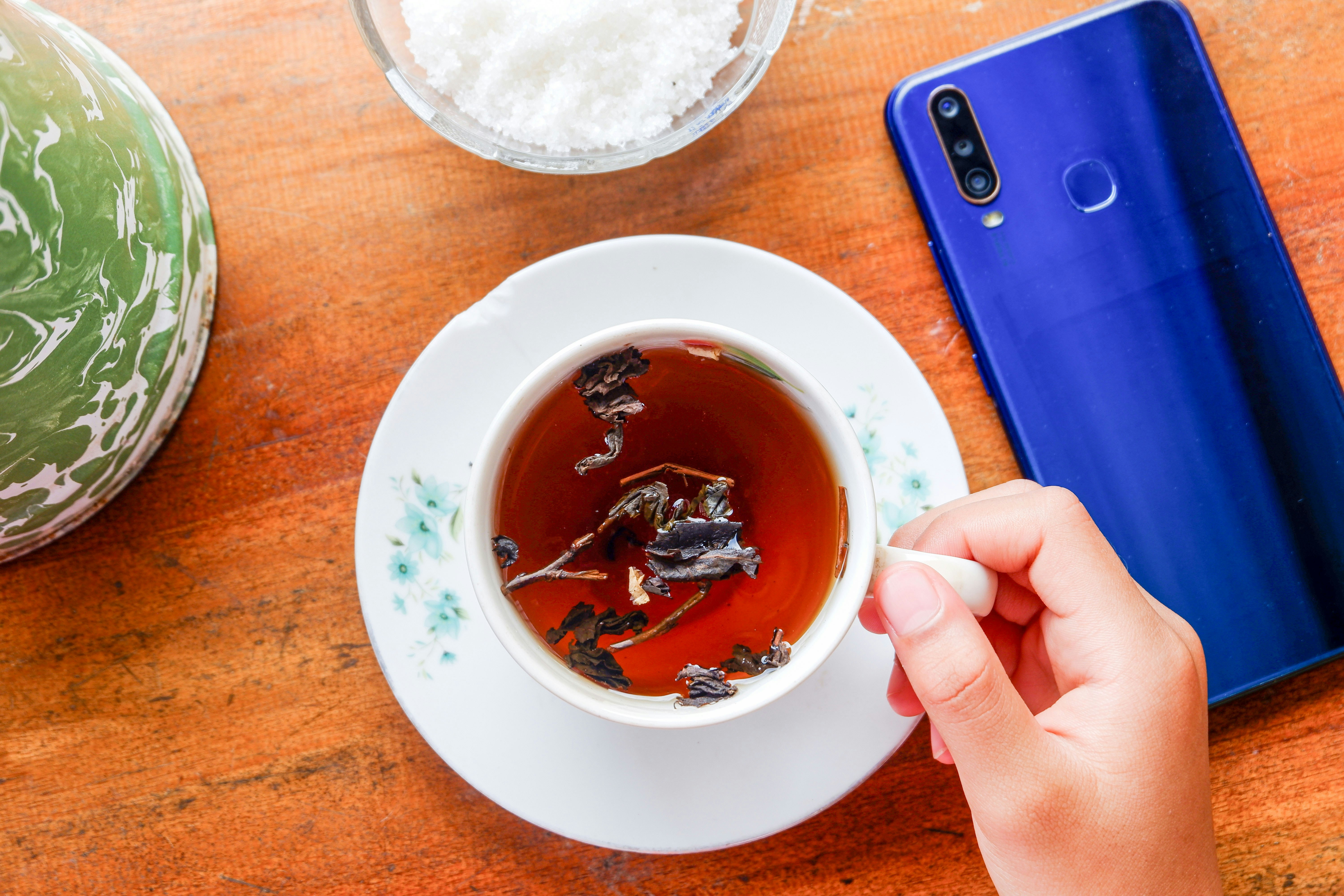 Top-Down Moment: Tea Cup, Hand, and a Blue Phone on Warm Wood