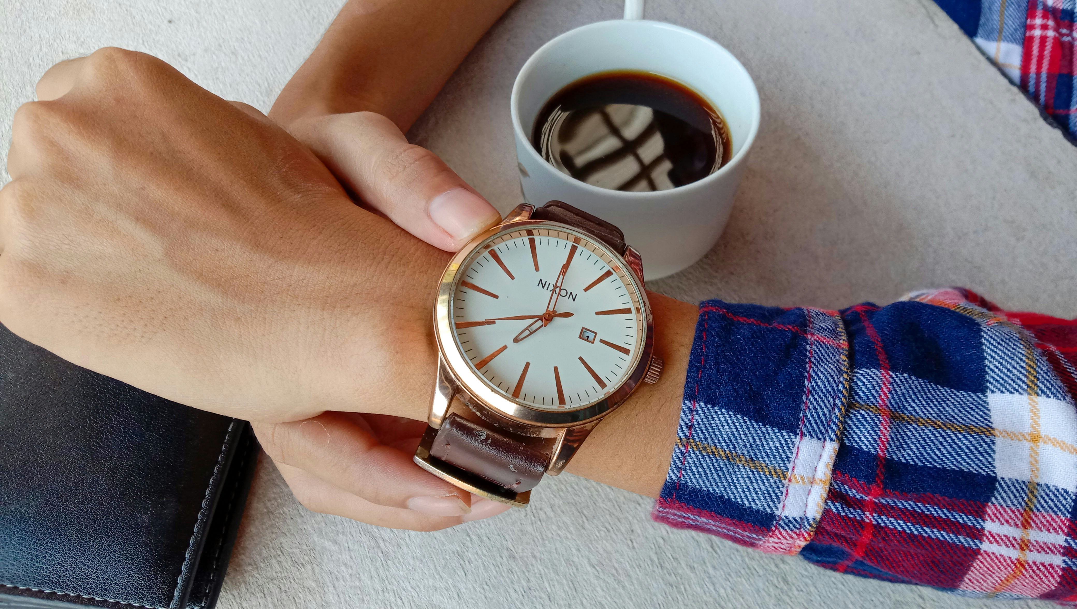 Photo of a person enjoying a cup of black coffee on a wooden table | A person wears a watch and has coffee.
