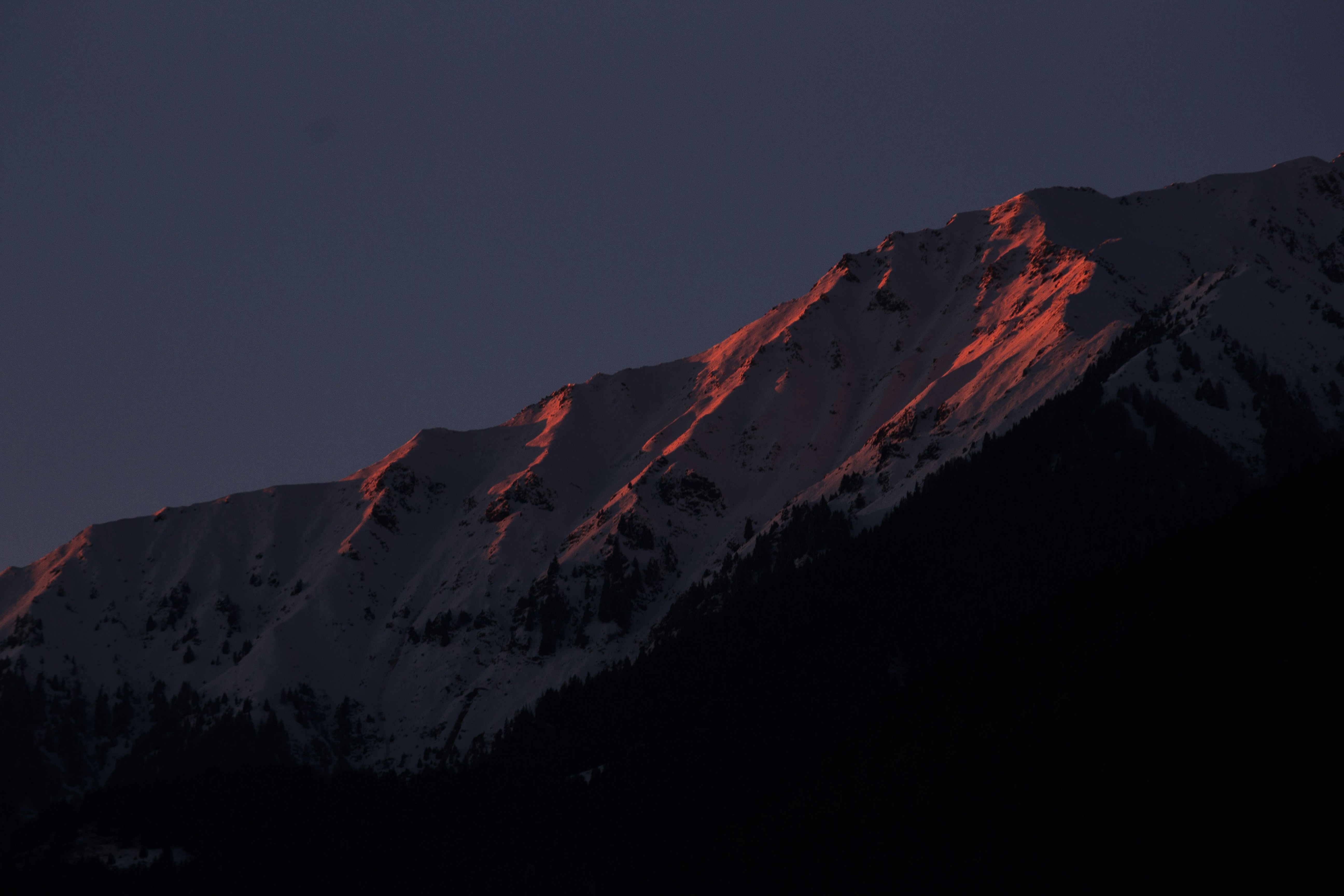 Sunset light illuminating the snow-capped peaks of a mountain range against a twilight sky.