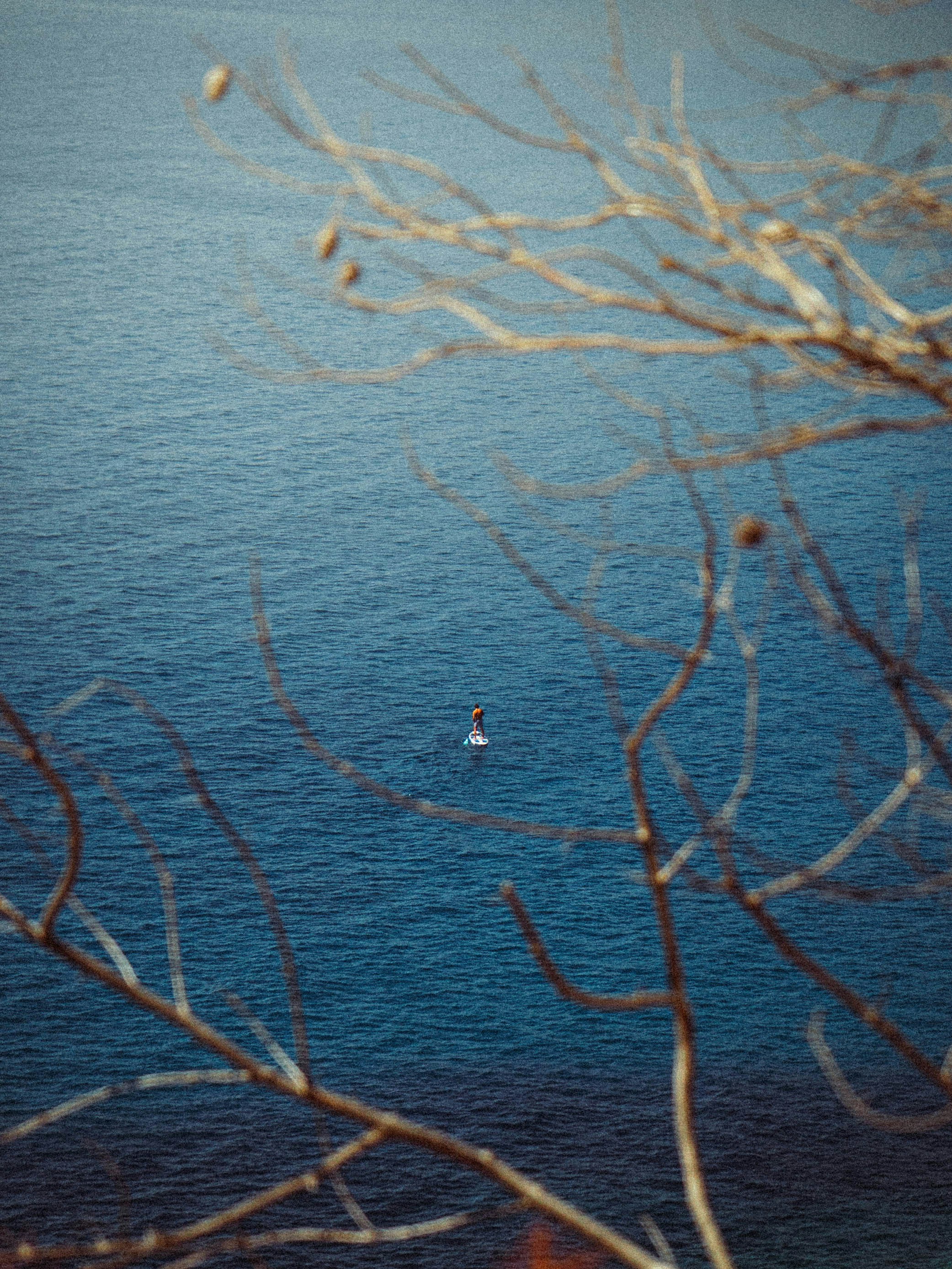 A lone paddleboarder floats on the deep blue sea. Summer holidays in Mallorca feel slow, serene, and sun-soaked. Nature, solitude, and salt in the air. | A person paddleboards on the open ocean.