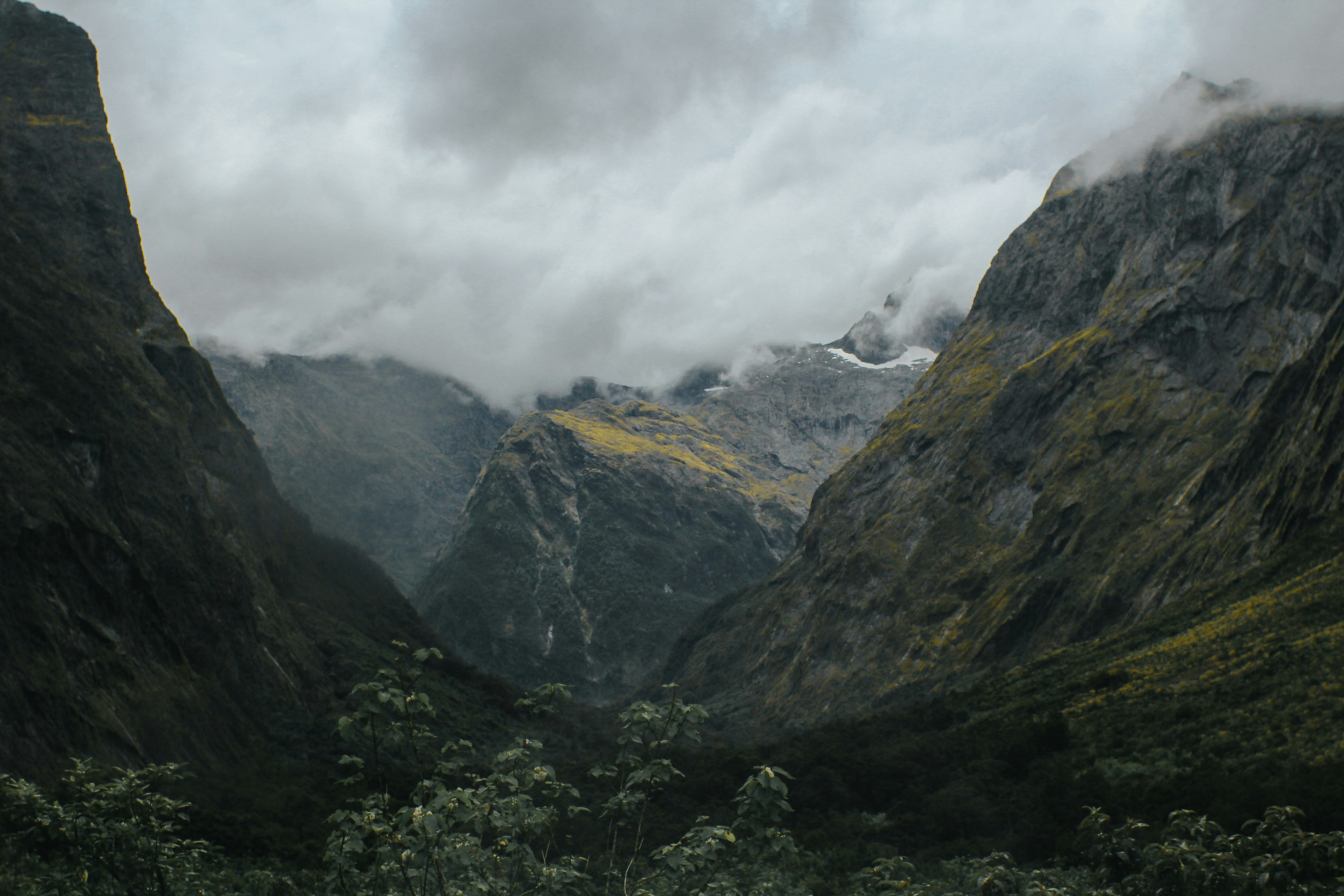 Dramatic mountain valley shrouded in clouds, showcasing rugged terrain and hints of greenery amidst the rocky landscape.