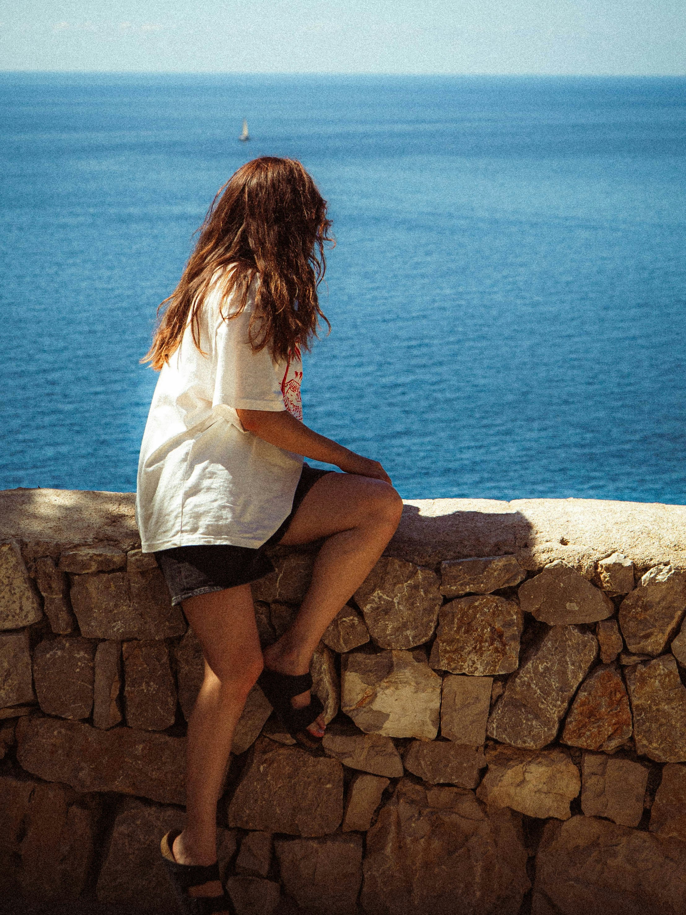 Stone Wall Solace: A Seaside Portrait Framed by the Blue Expanse