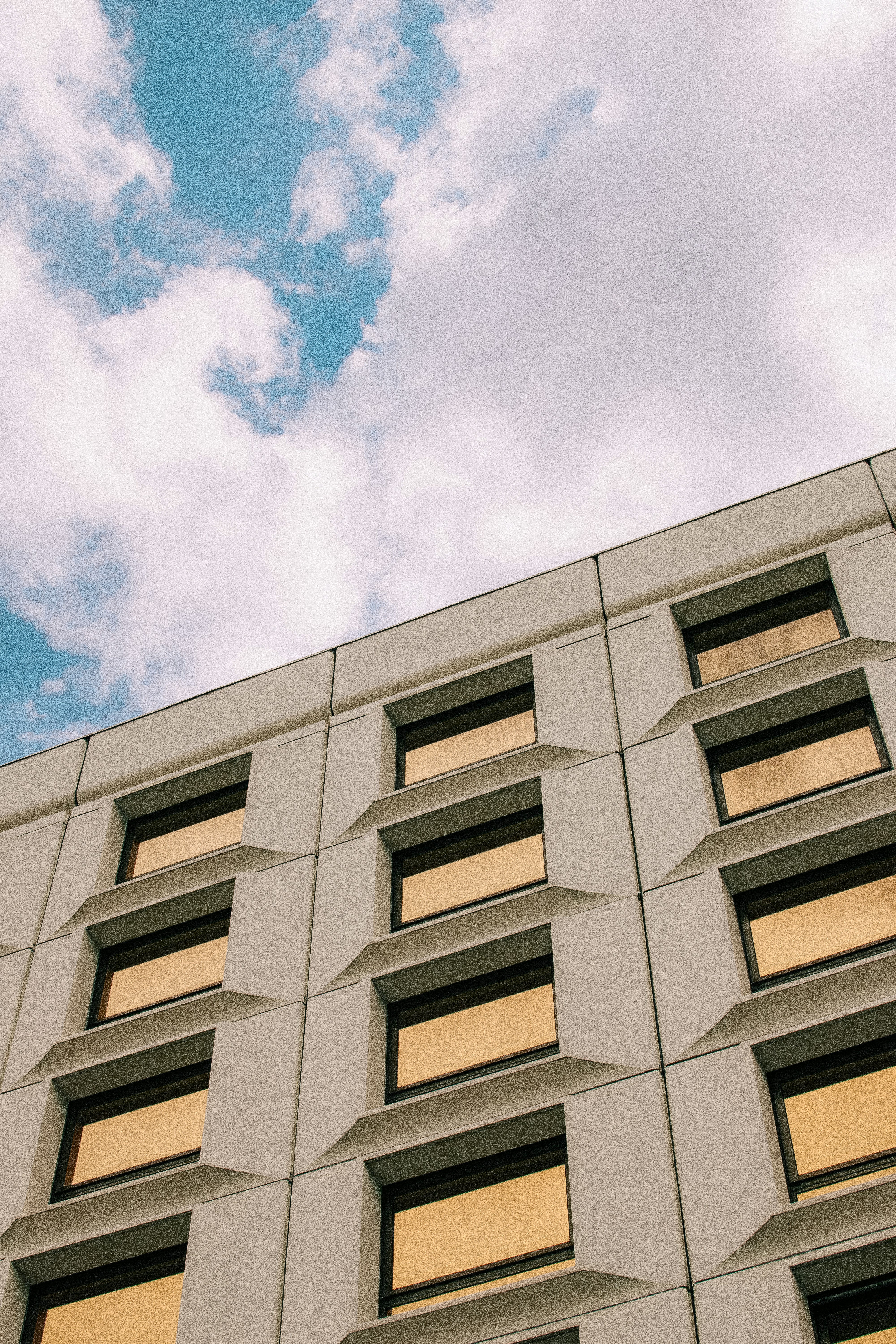 Modern building facade with geometric patterns reflecting sunlight against a cloudy sky.