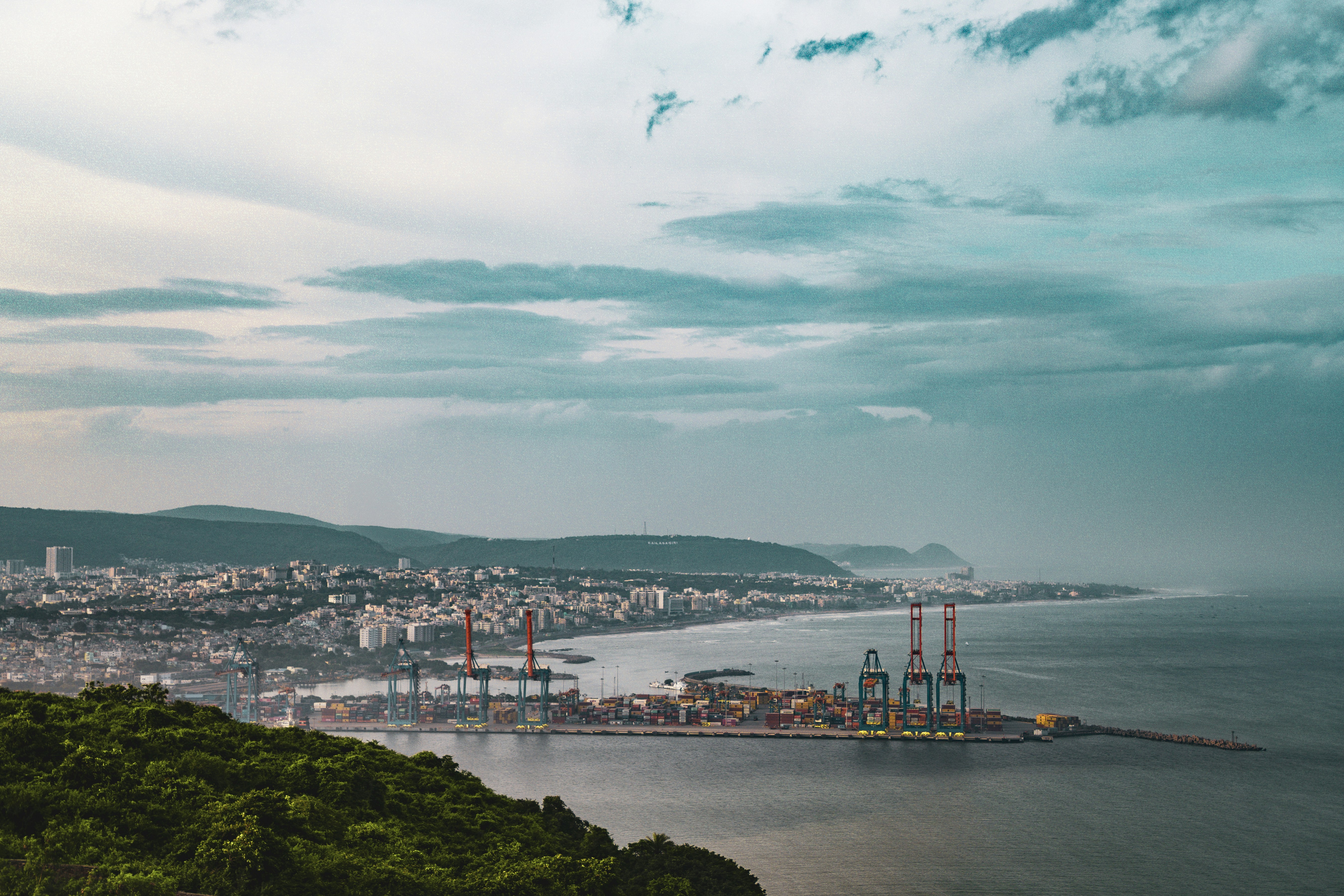 A harbor town sprawls along the coast under cloudy skies.