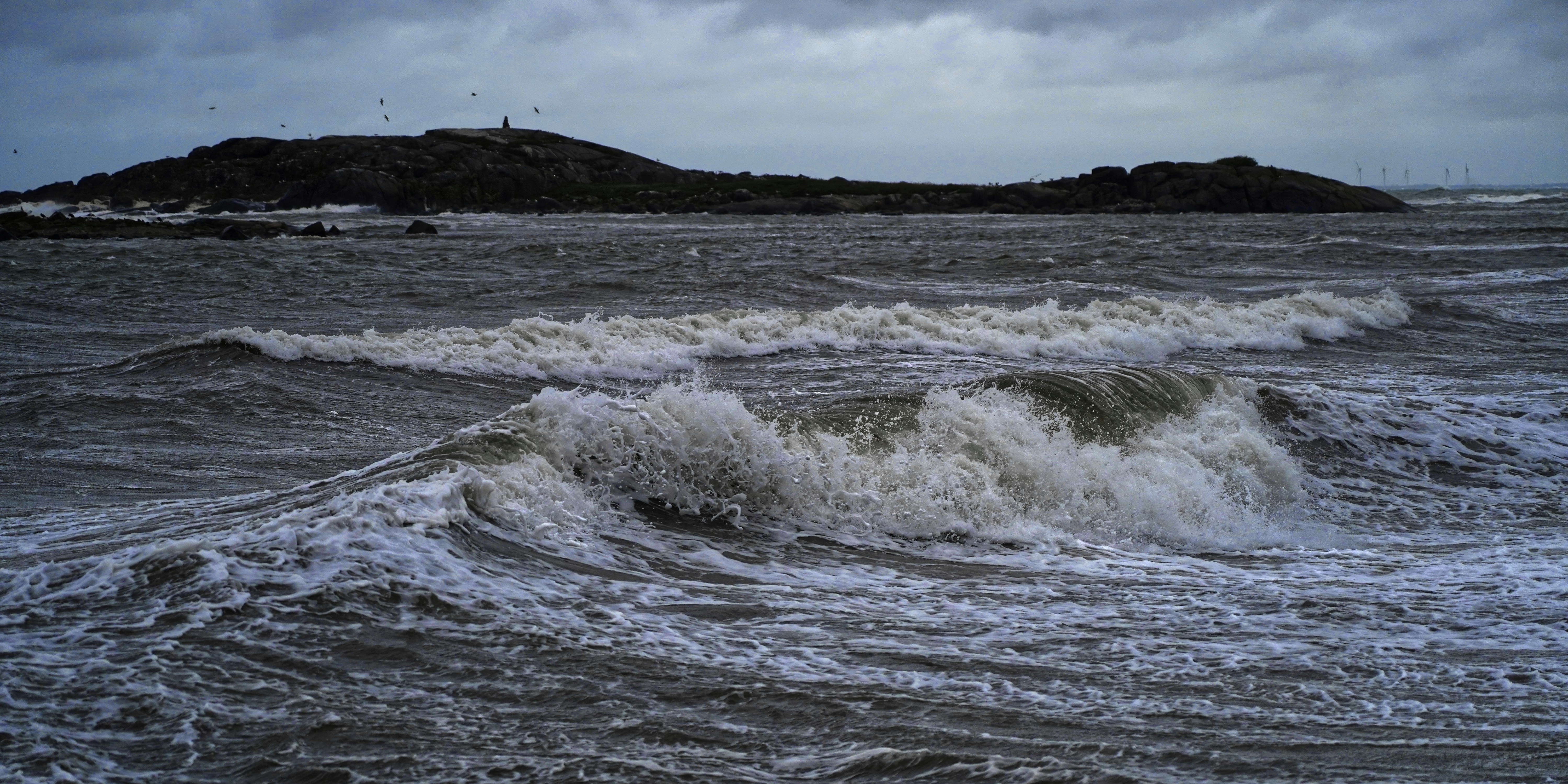 Rough waves crash near an island under a stormy sky.