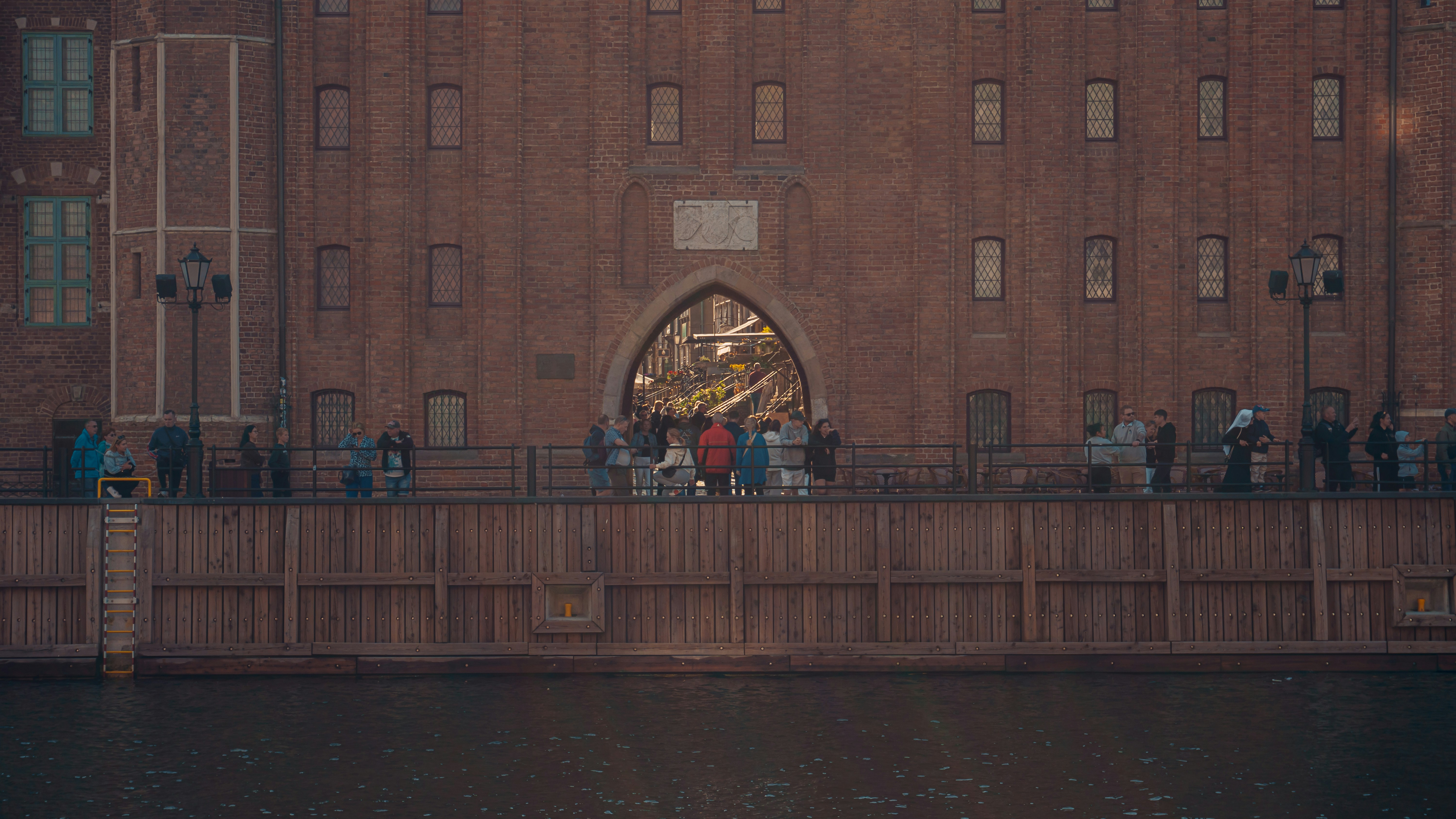 People gather around a brick building near the water.