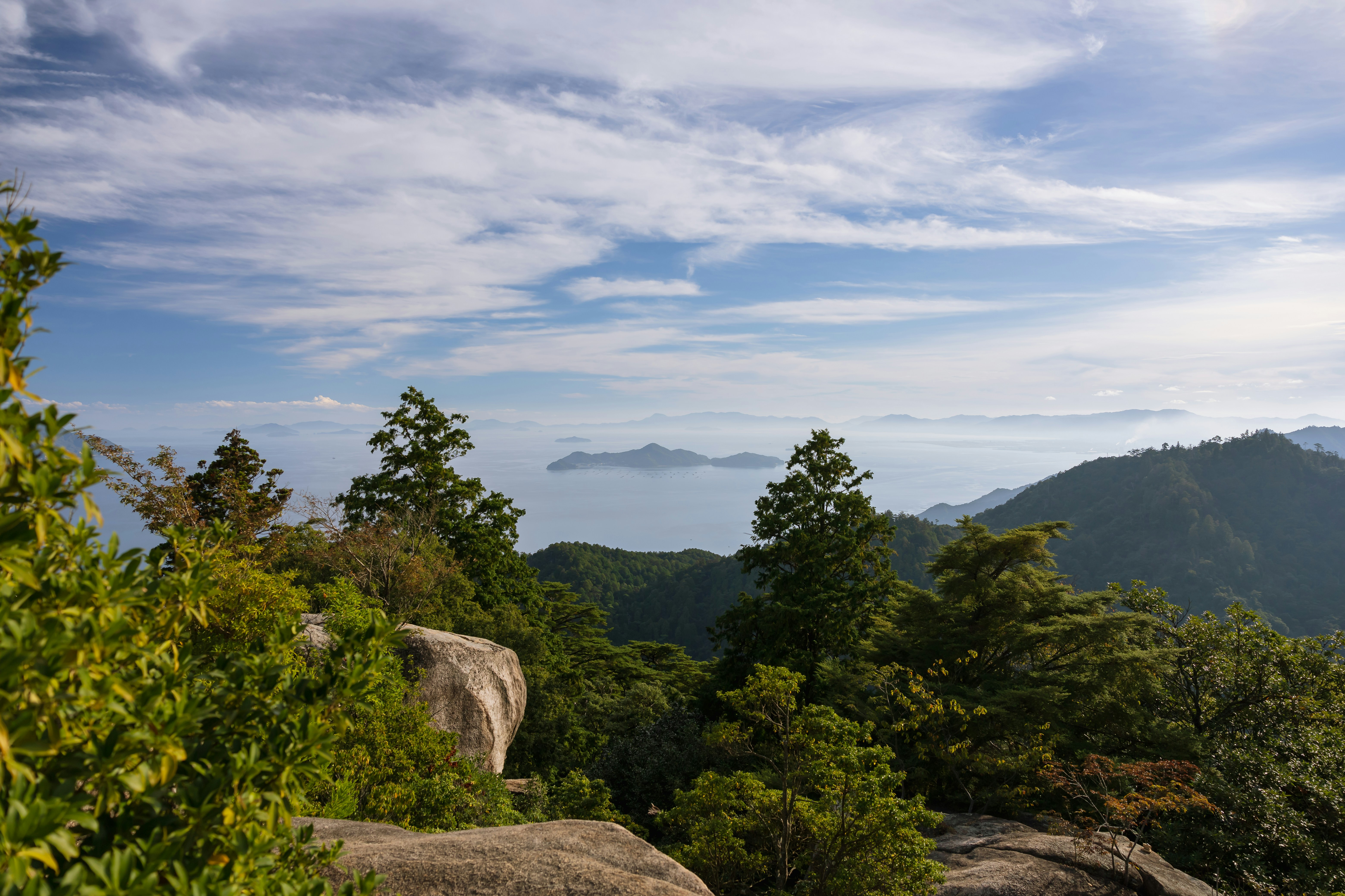Lush trees frame a tranquil view of distant islands shrouded in mist, with a clear sky above. This landscape captures the serene beauty of nature's embrace.