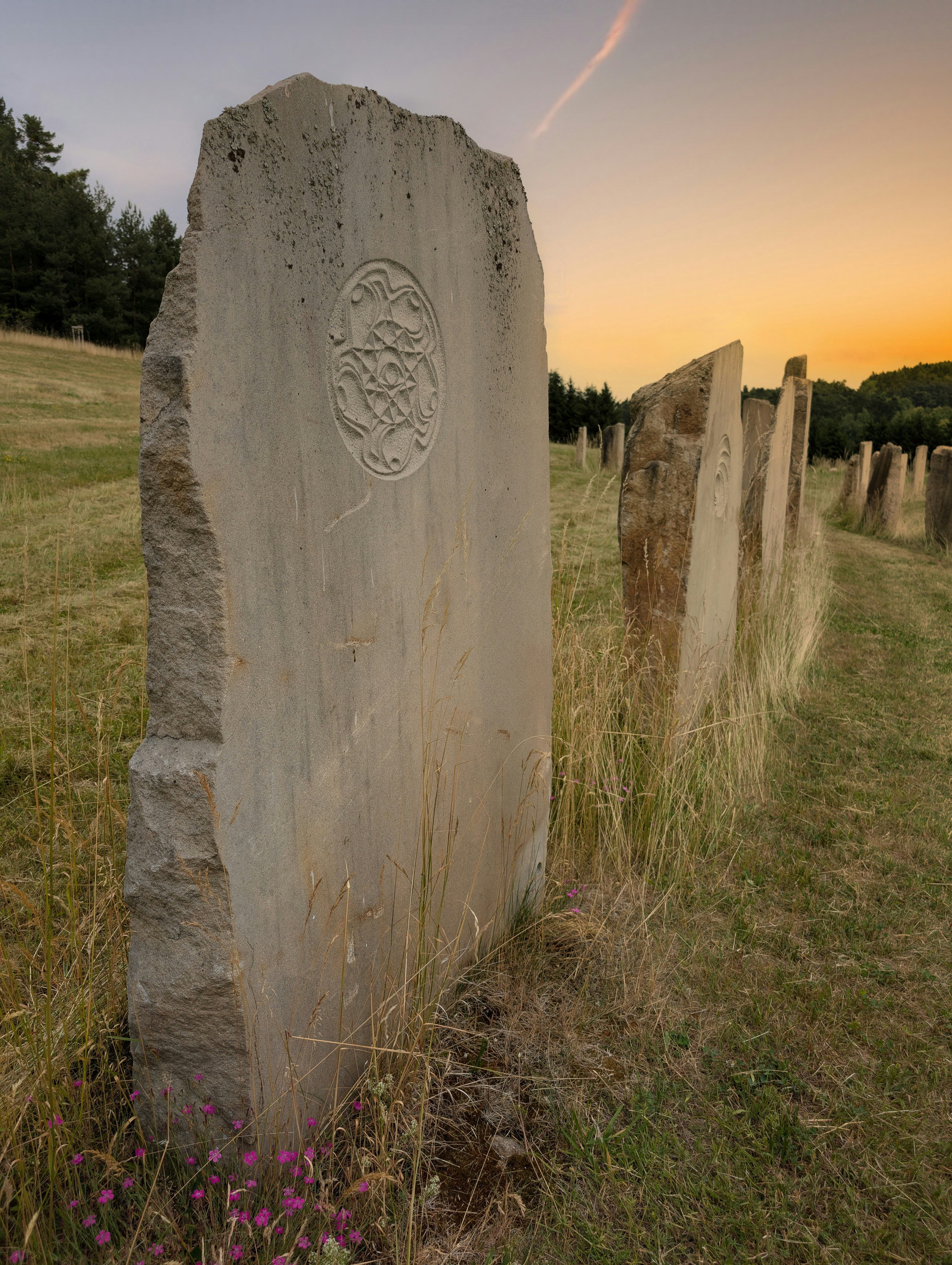 Stone monoliths stand in a grassy field at sunset.