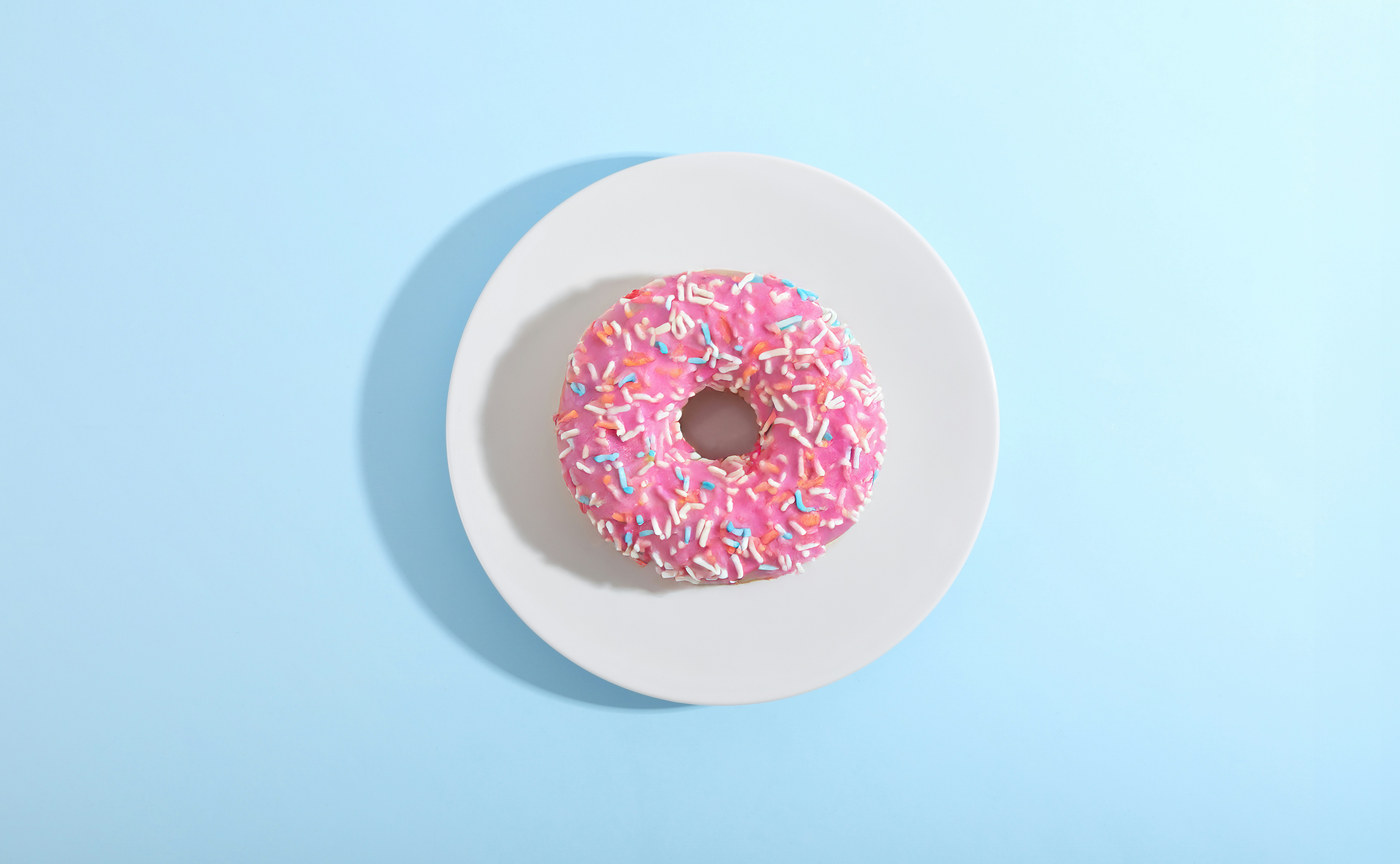 A pink donut sits on a white plate.