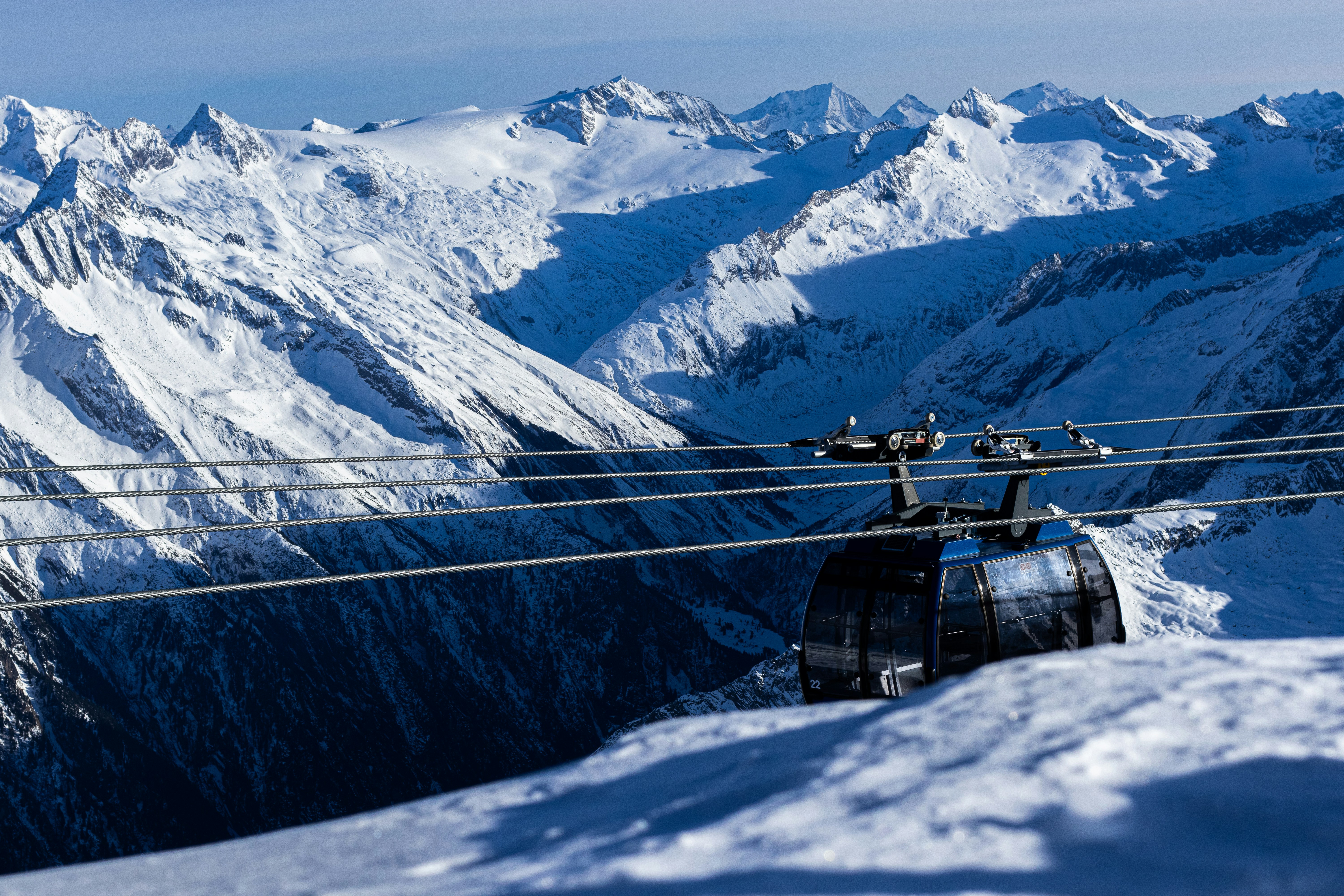 Ski lift in the mountains | A gondola travels across snowy, mountainous terrain.