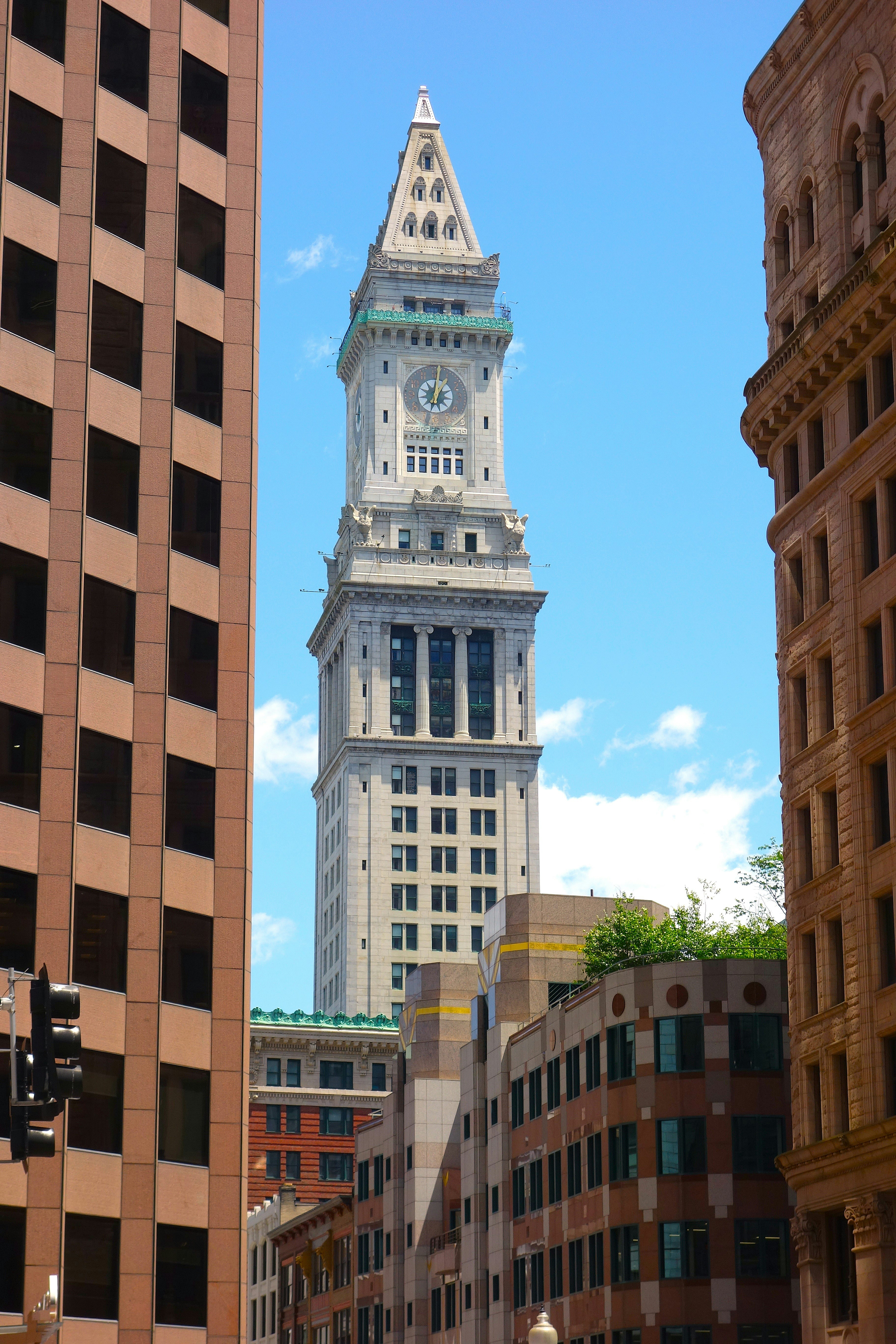 Historic clock tower rising majestically between modern buildings under a clear blue sky.
