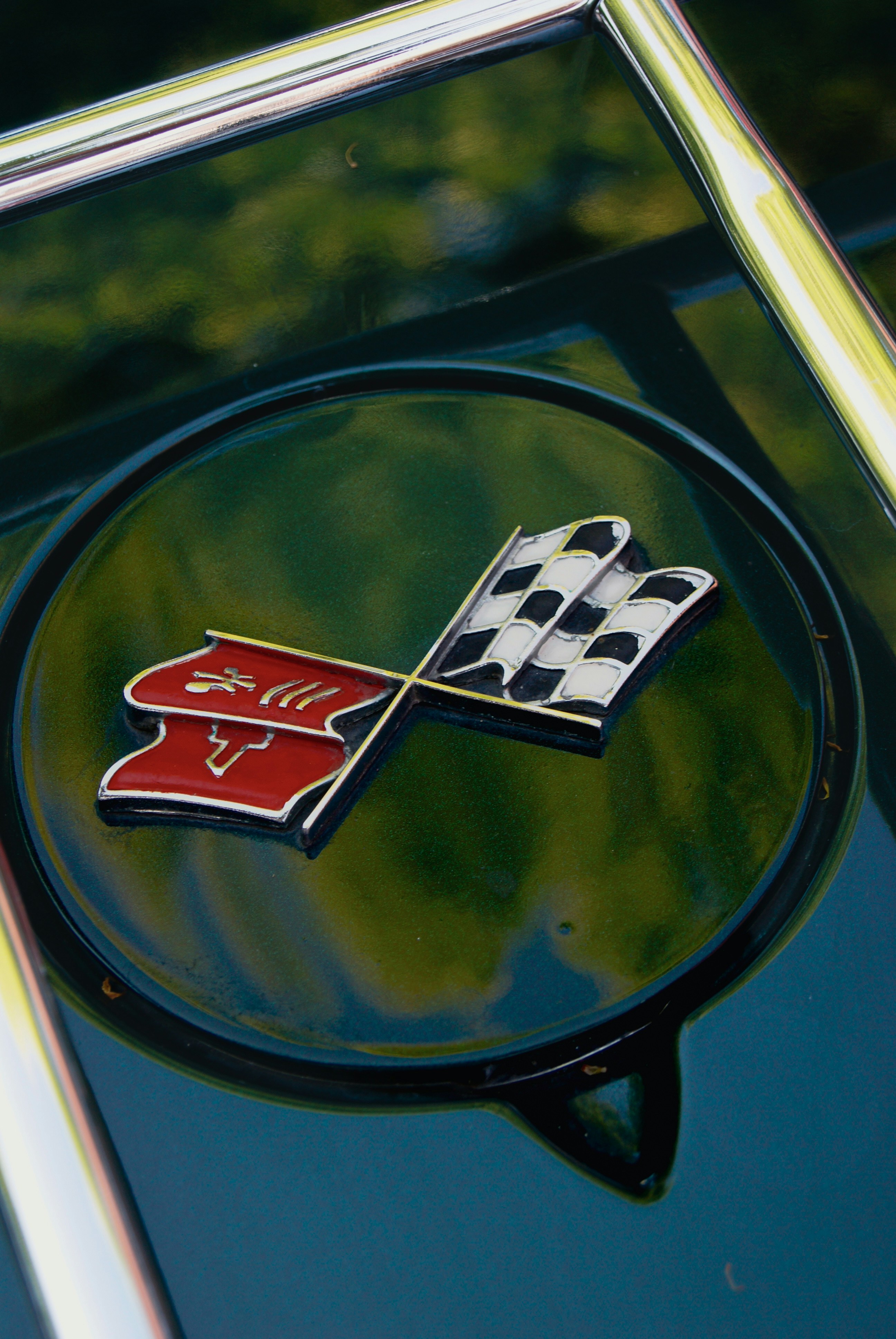 Close-up of the Chevrolet Corvette emblem featuring a crossed flag design, reflecting the surrounding environment.