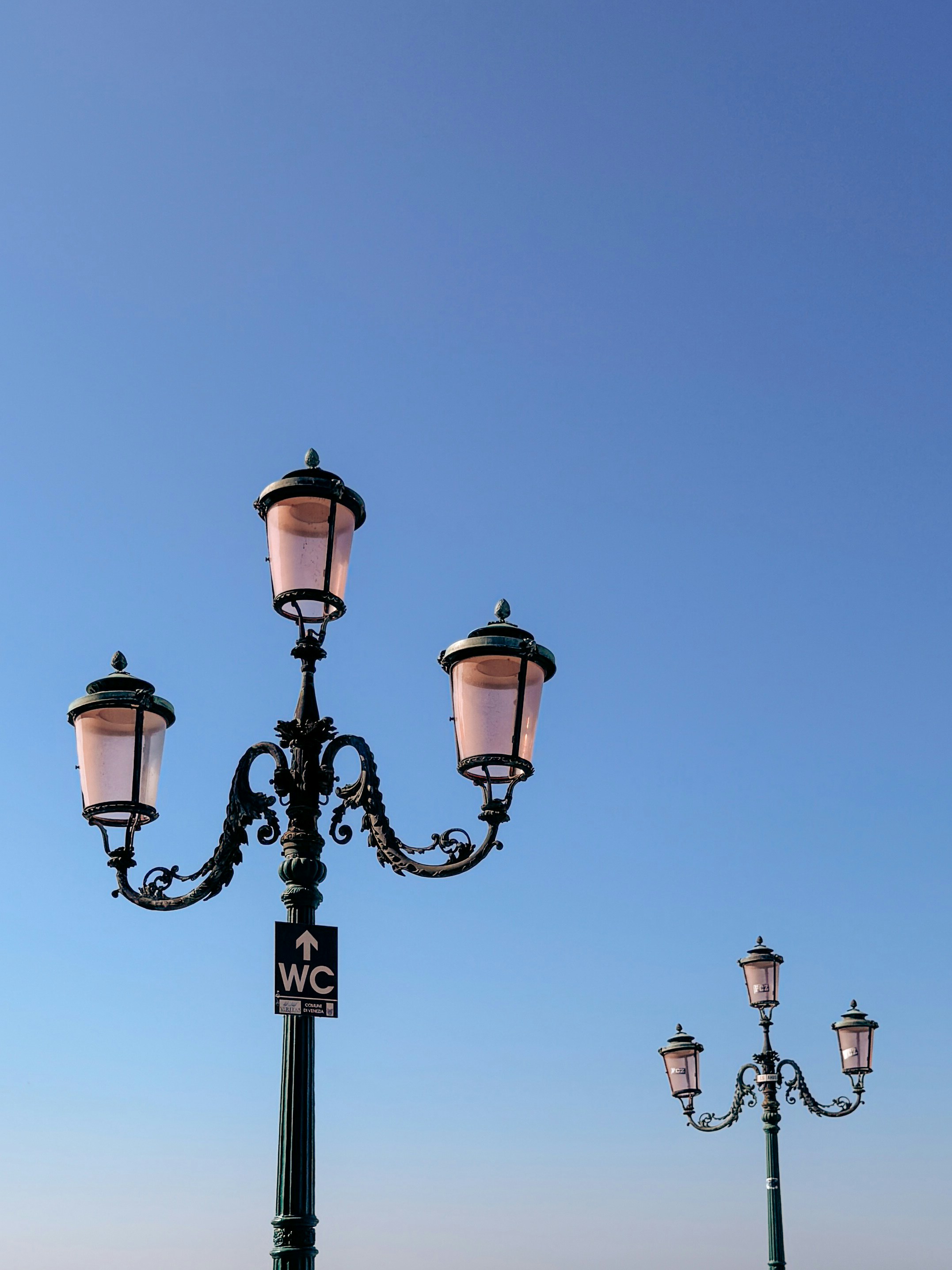 Two ornate street lamps against a clear, blue sky.