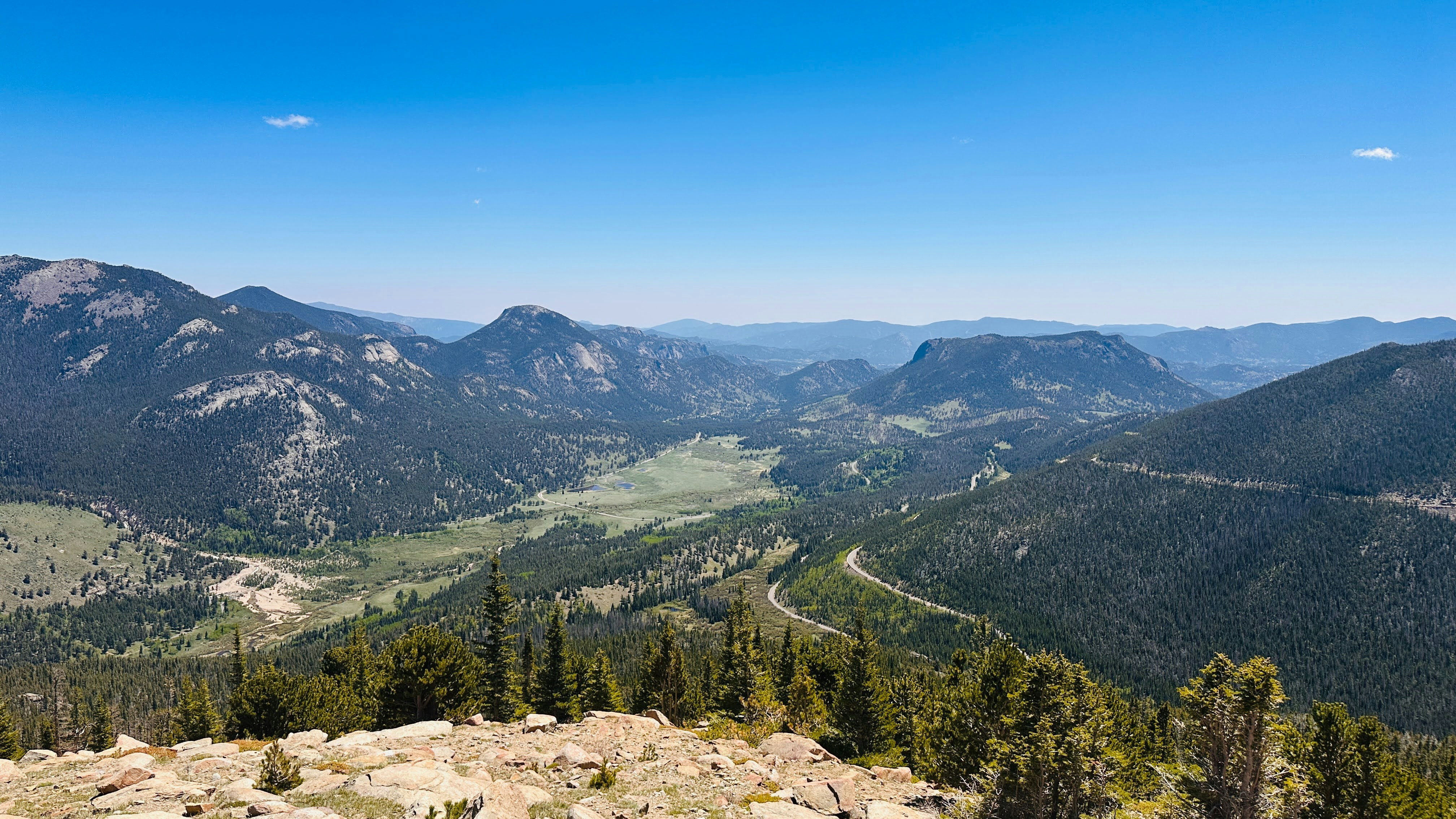 Expansive mountain landscape showcasing lush valleys and winding roads under a clear blue sky.