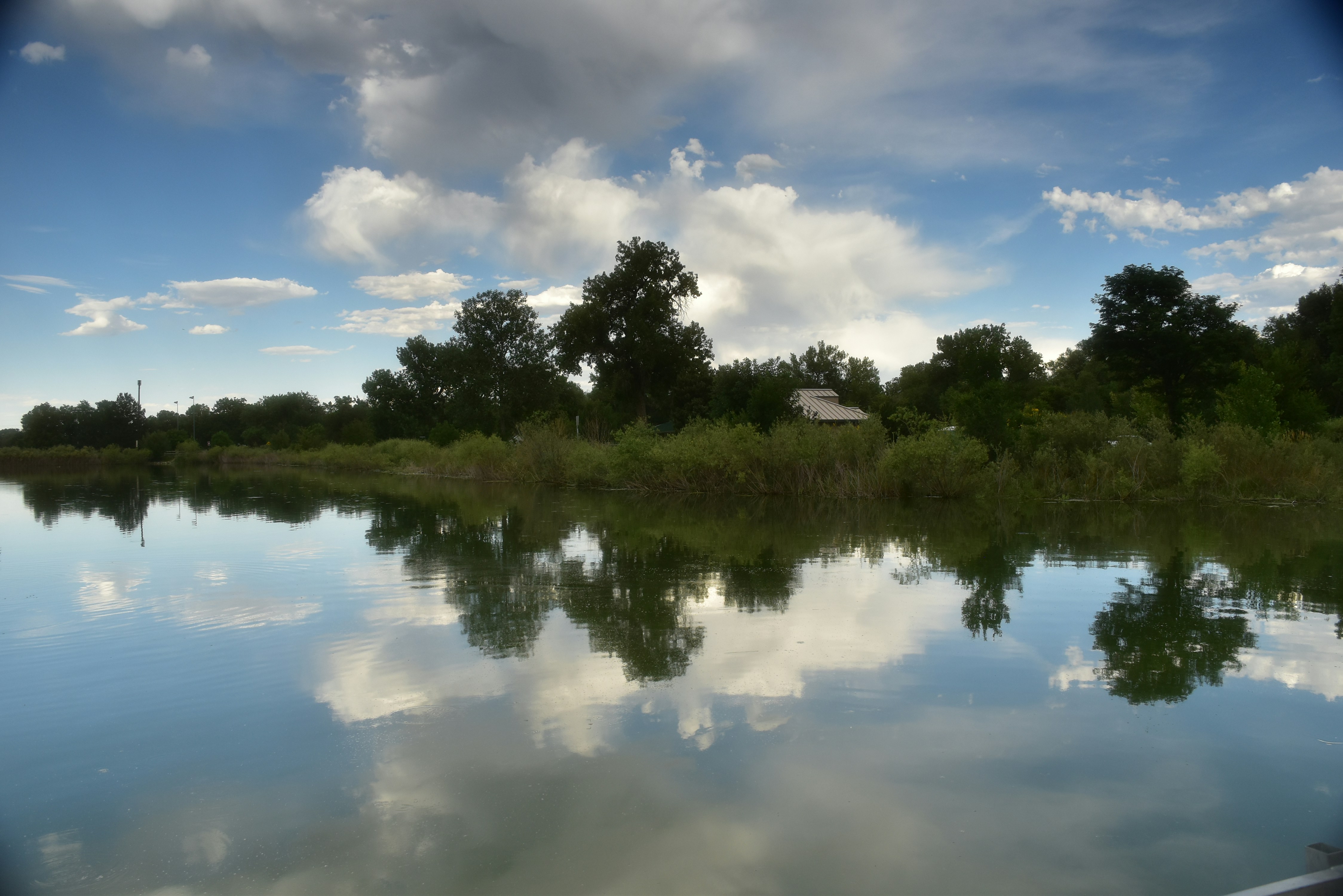 Clouds and trees are reflected in the calm water.