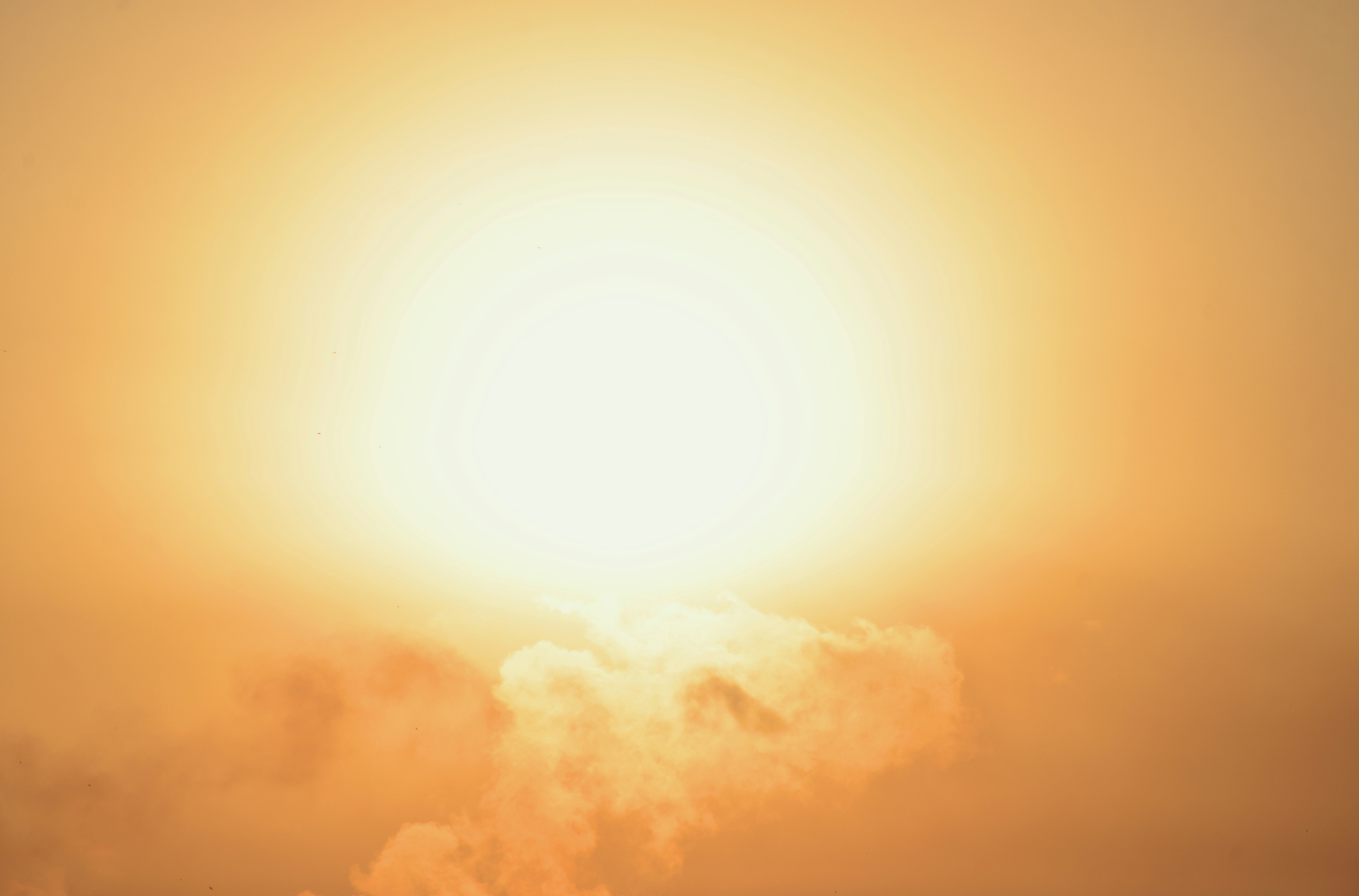 Vibrant sun radiating through a soft haze, merging with wisps of clouds in a serene sky.