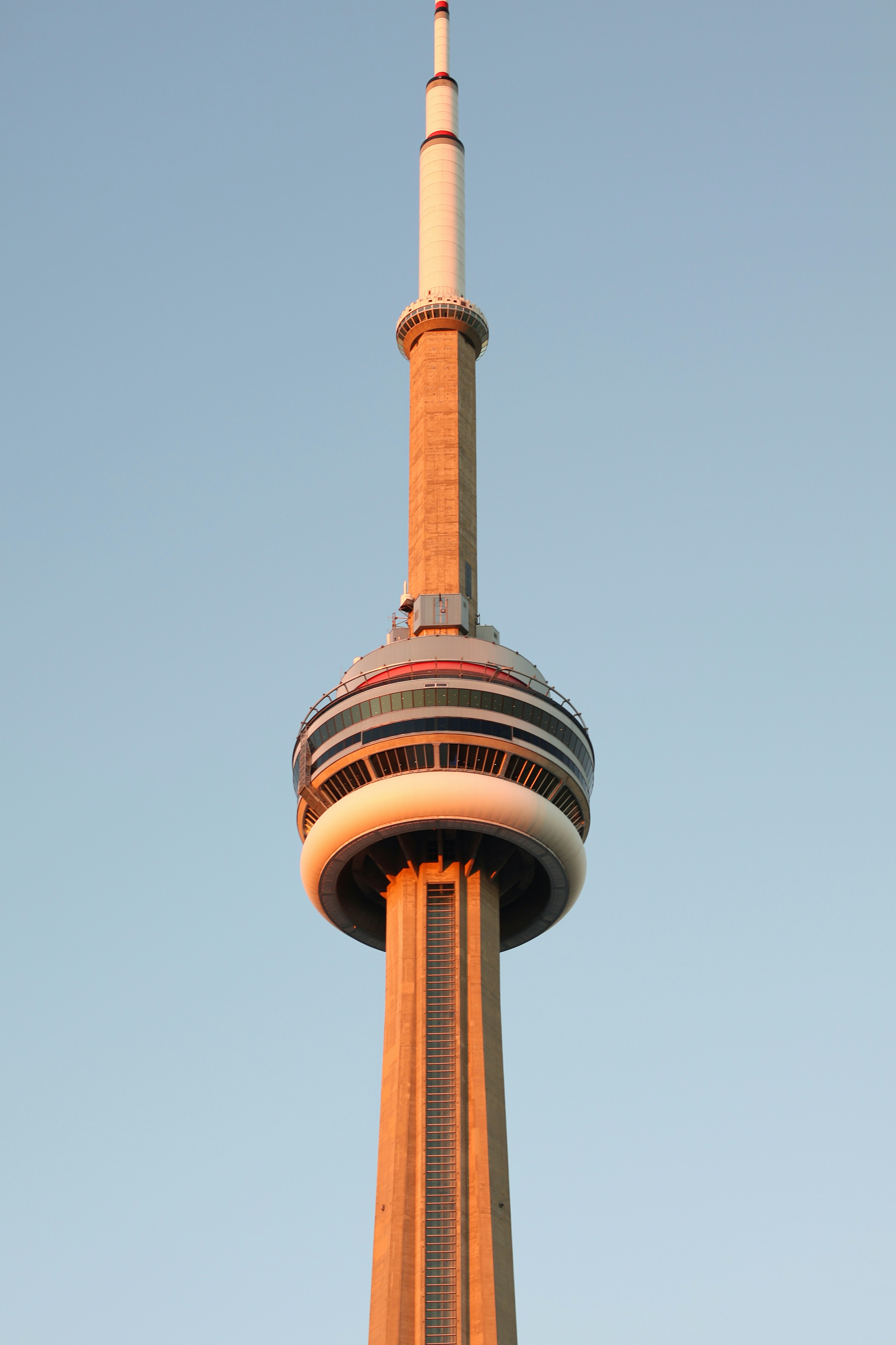 View of the CN Tower in Toronto, Canada from below during golden hour | The cn tower stands tall against a clear sky.
