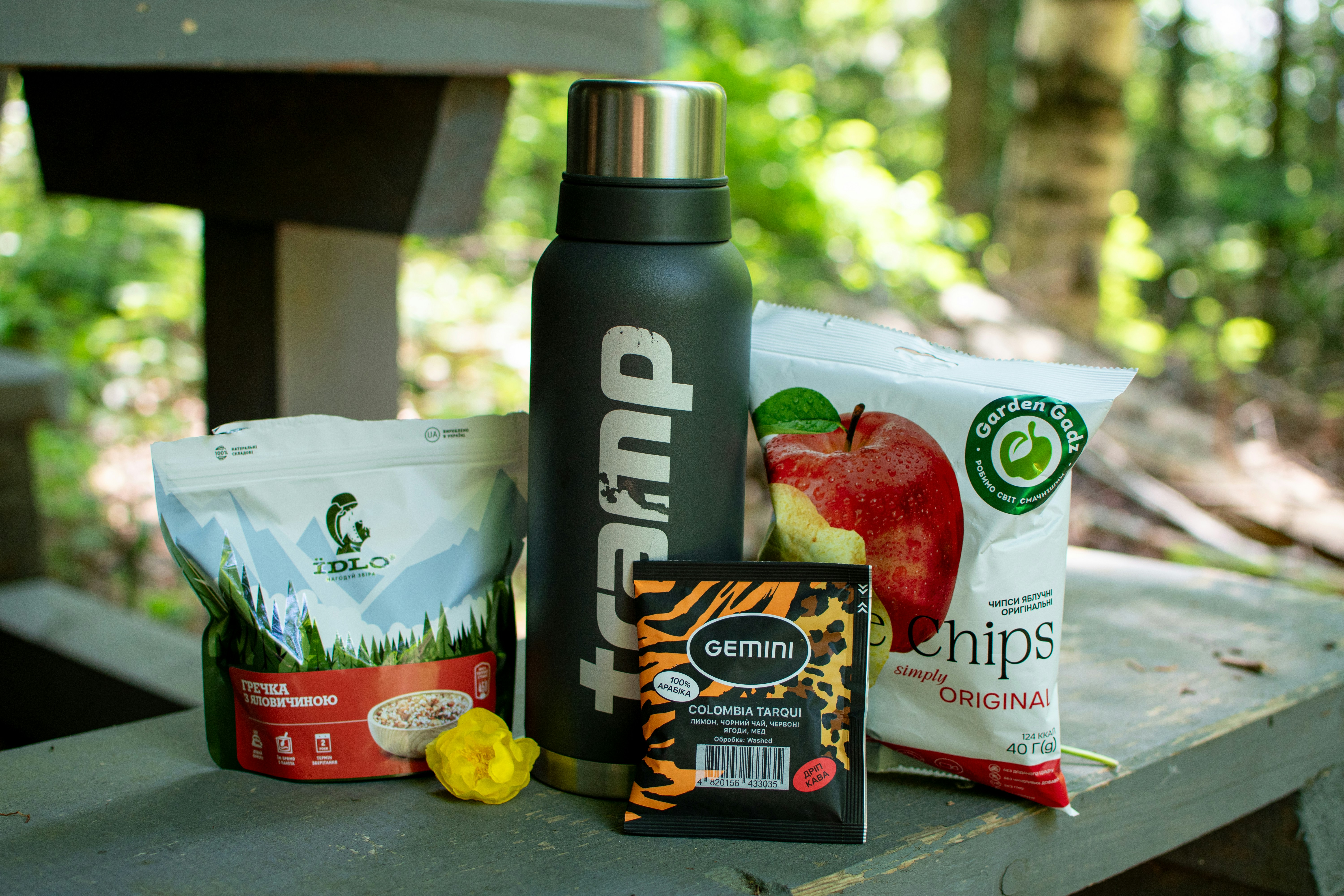 An assortment of snacks and a water bottle arranged on a wooden surface in a lush green forest setting.