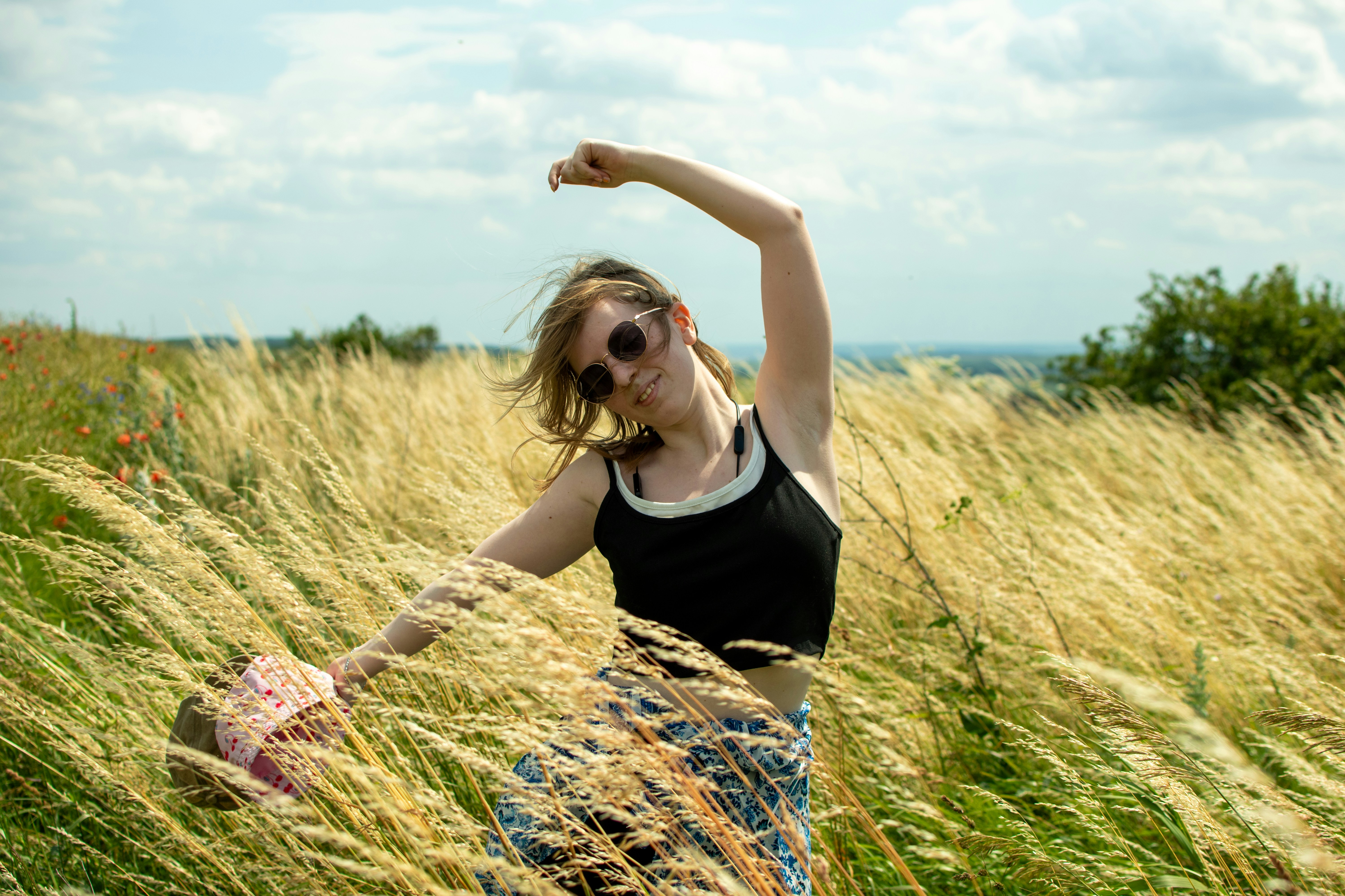 A young woman dances playfully amidst tall golden grasses under a bright sky, exuding a sense of freedom and joy.