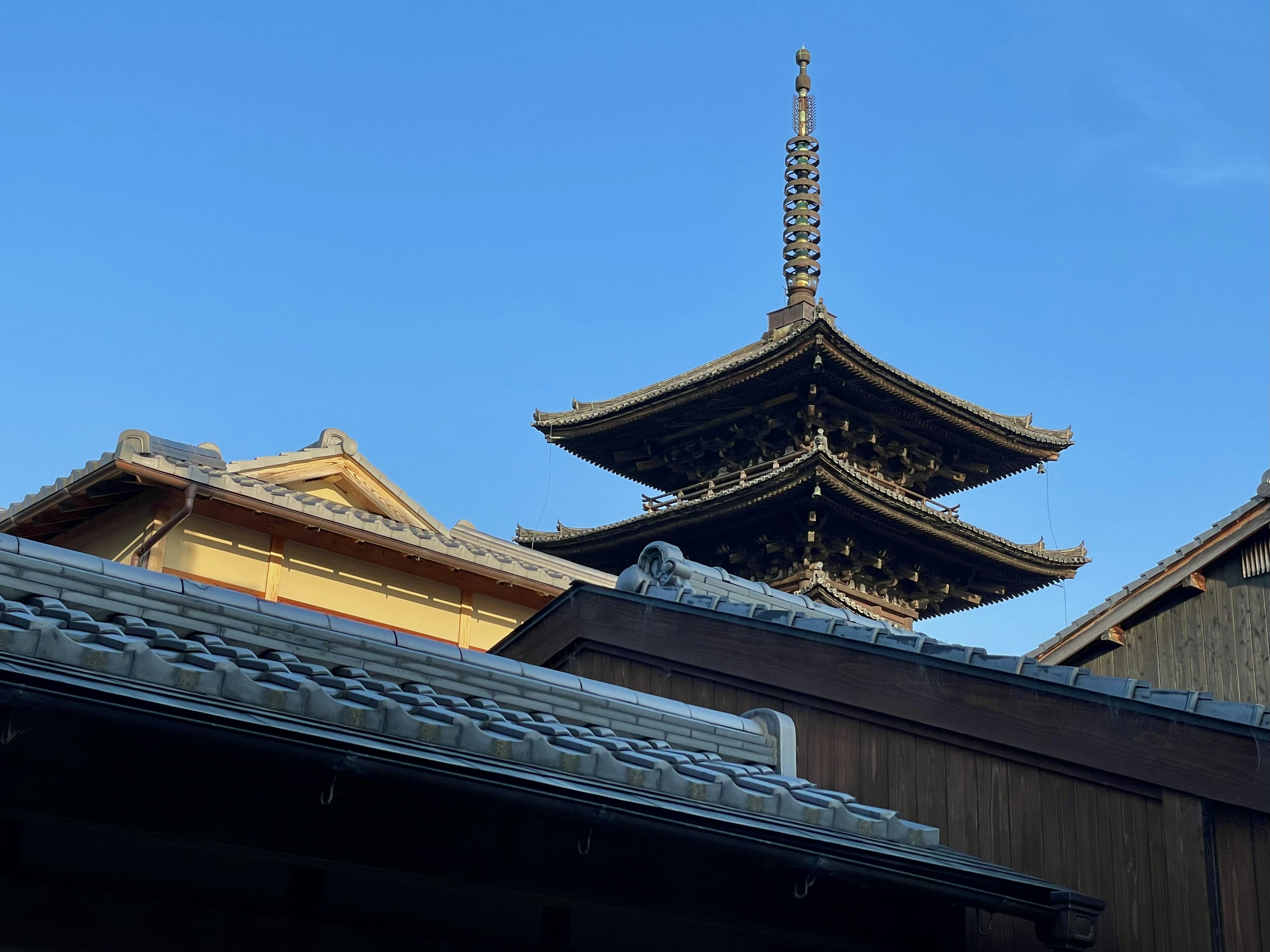 A traditional pagoda rises above wooden rooftops under a clear blue sky, showcasing architectural elegance and cultural heritage.