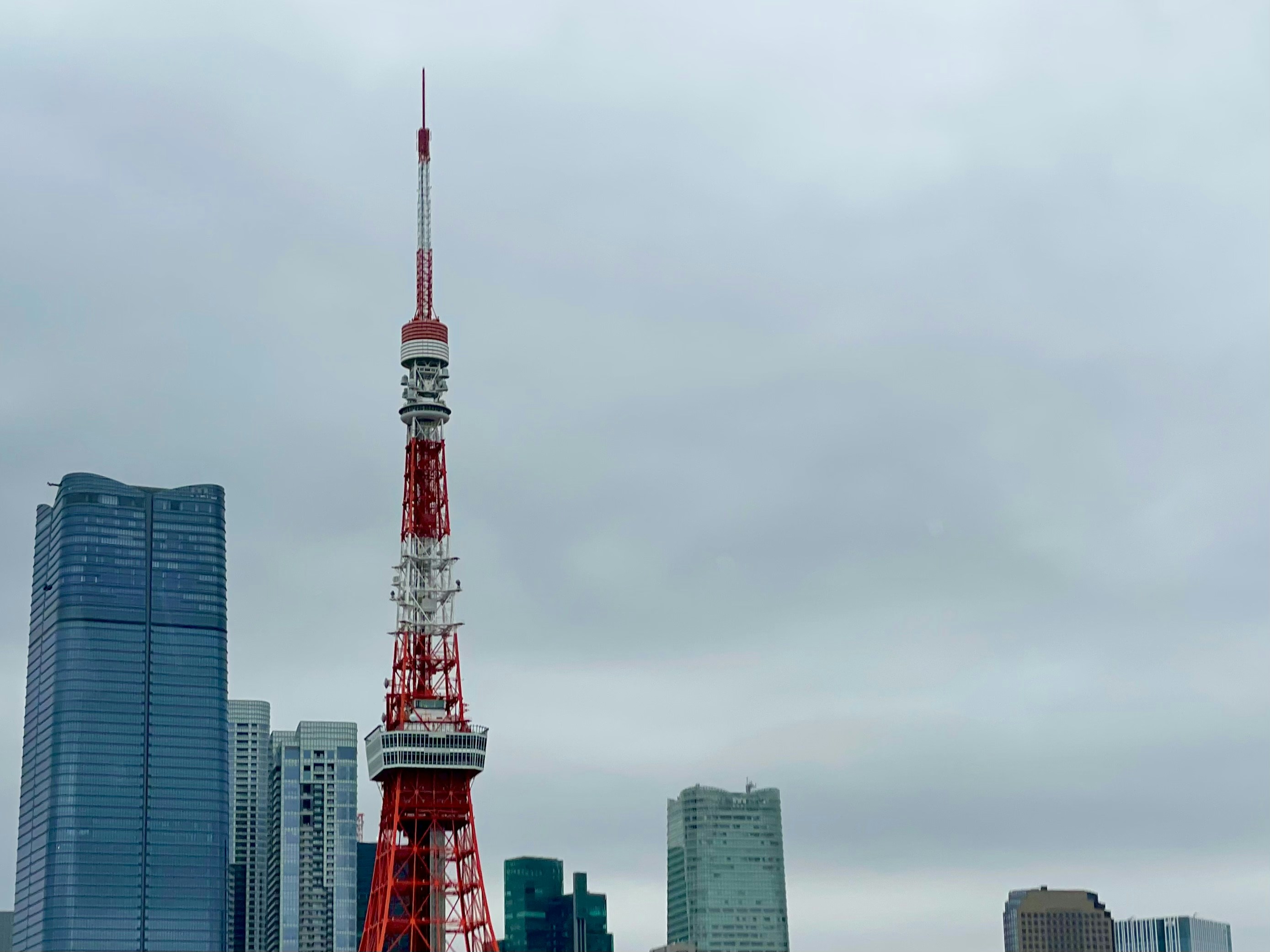 Tokyo Tower rising prominently against a backdrop of modern skyscrapers under a cloudy sky.