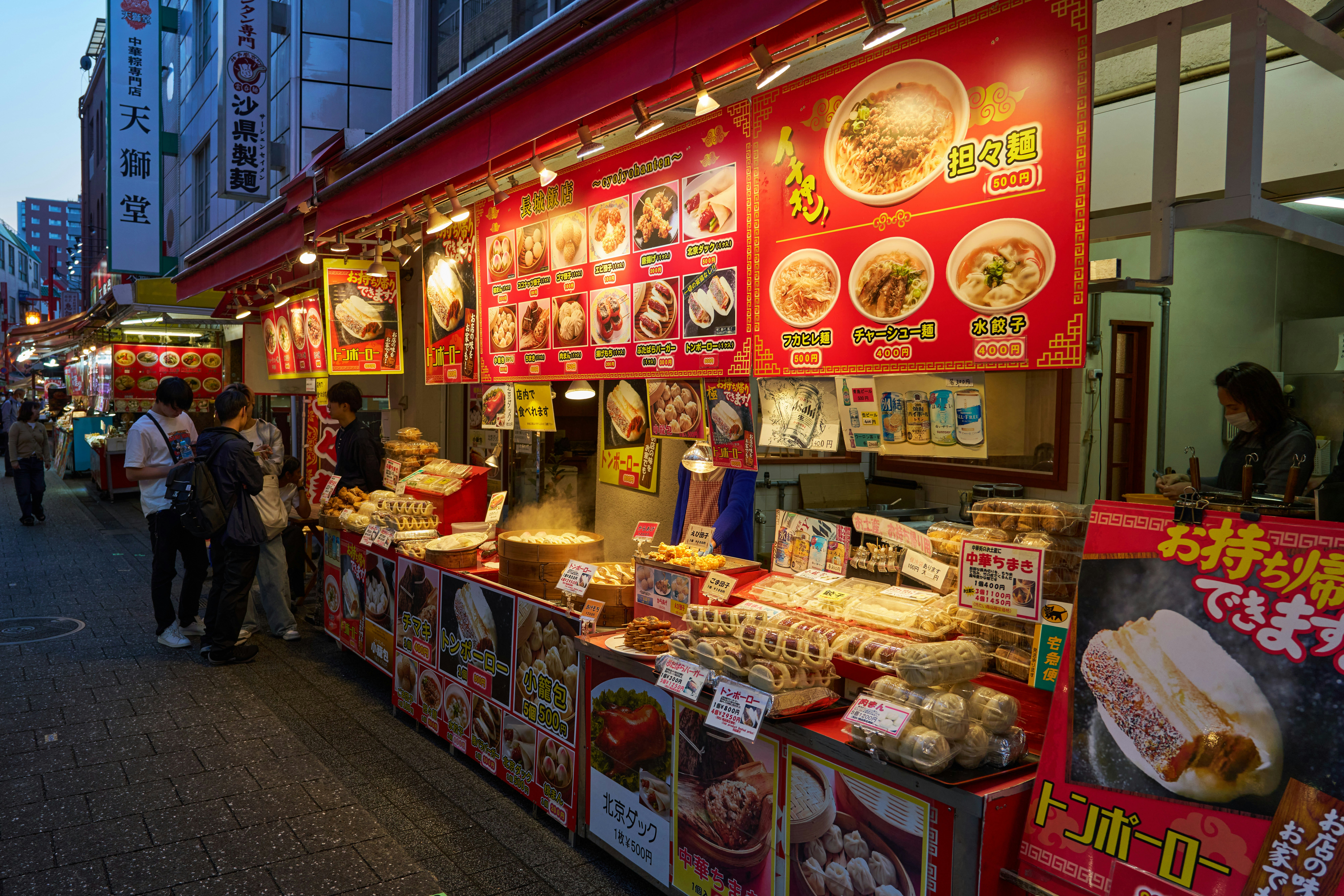Vibrant street food stall adorned with colorful menus and dishes, bustling with customers in an evening market. A mix of traditional and modern culinary offerings are showcased.