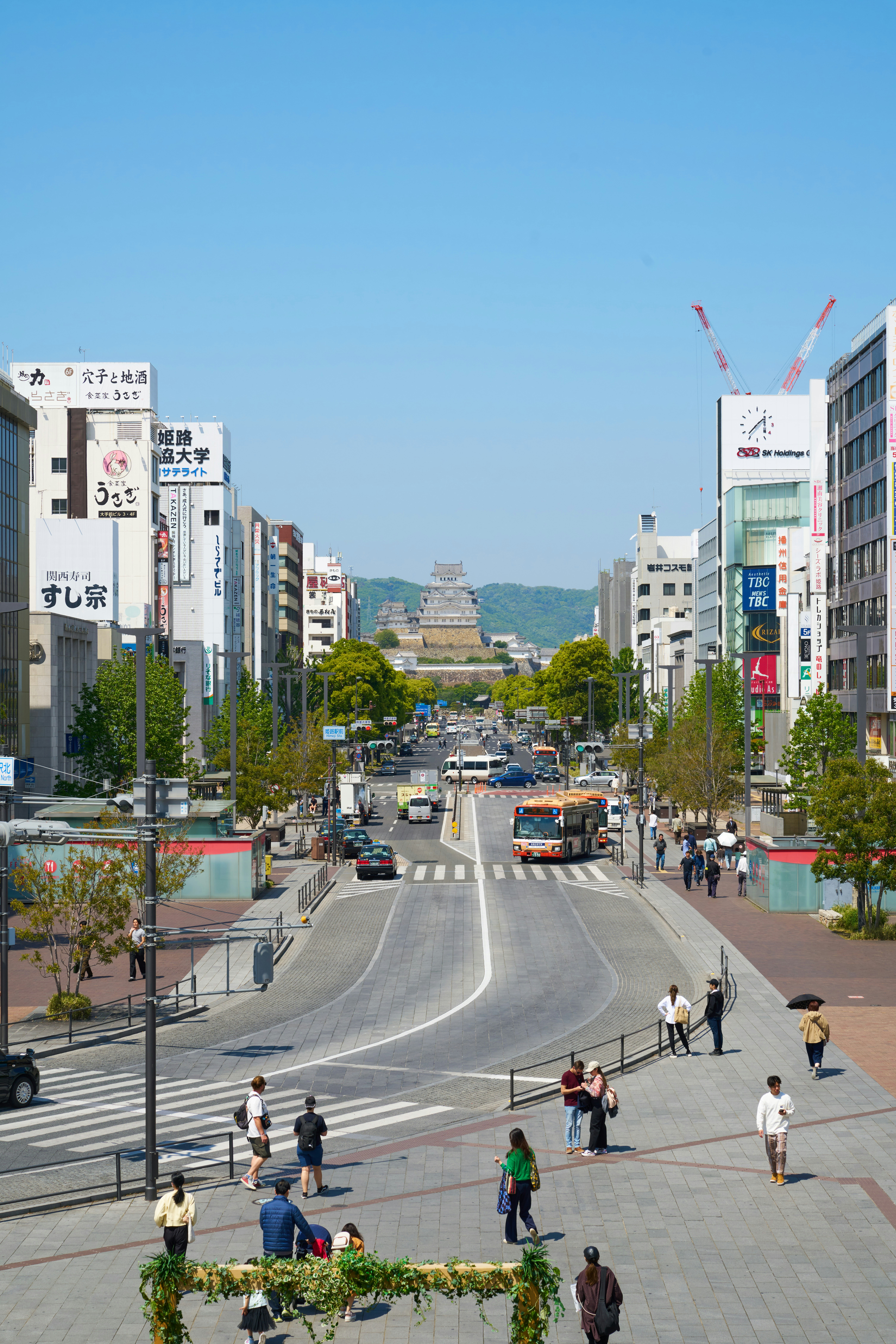 Vibrant city street leading towards a historic castle, framed by modern architecture and lively pedestrians. The scene captures the blend of tradition and contemporary life.
