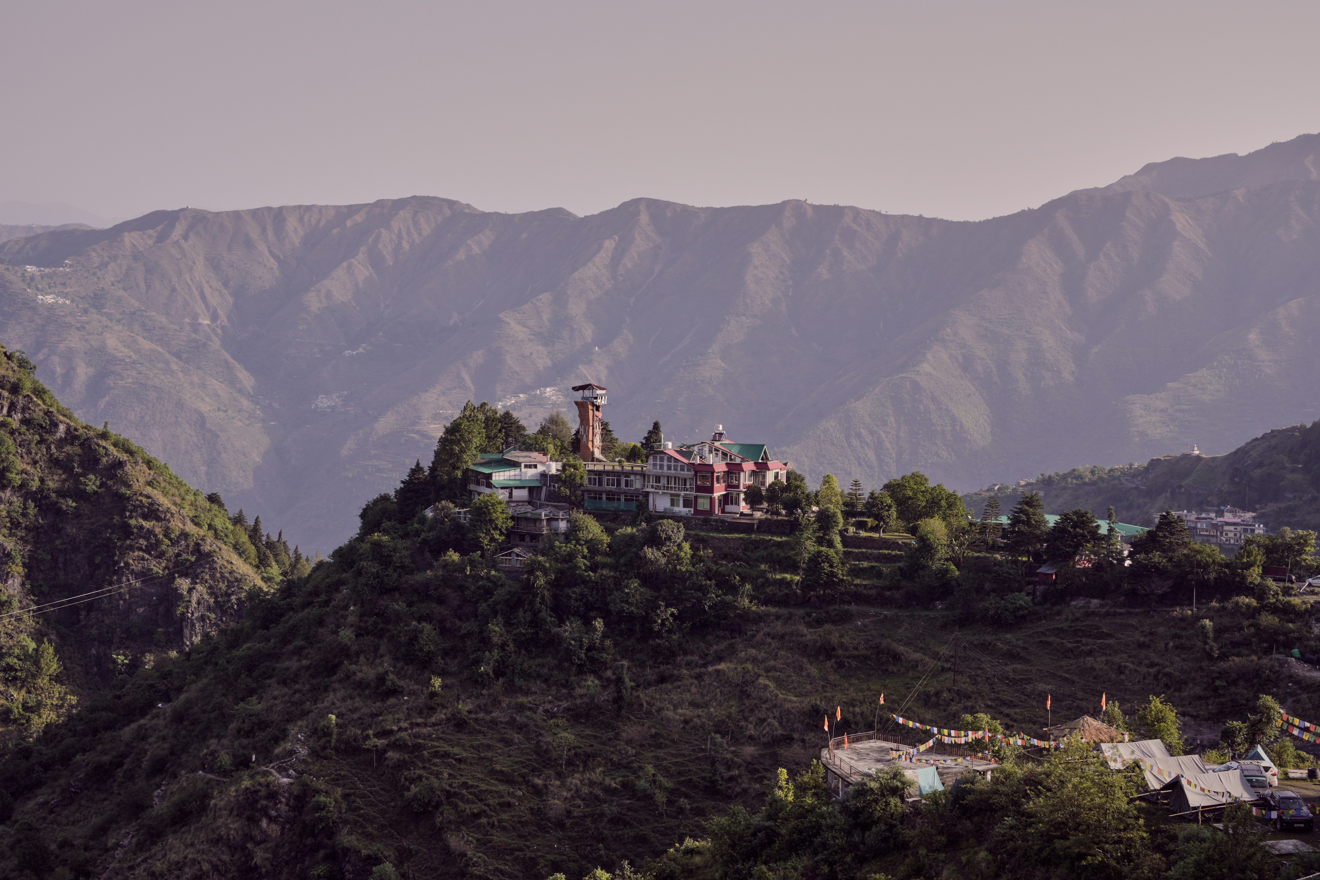 A picturesque mountain retreat nestled atop a hill, surrounded by lush greenery and majestic peaks in the background.