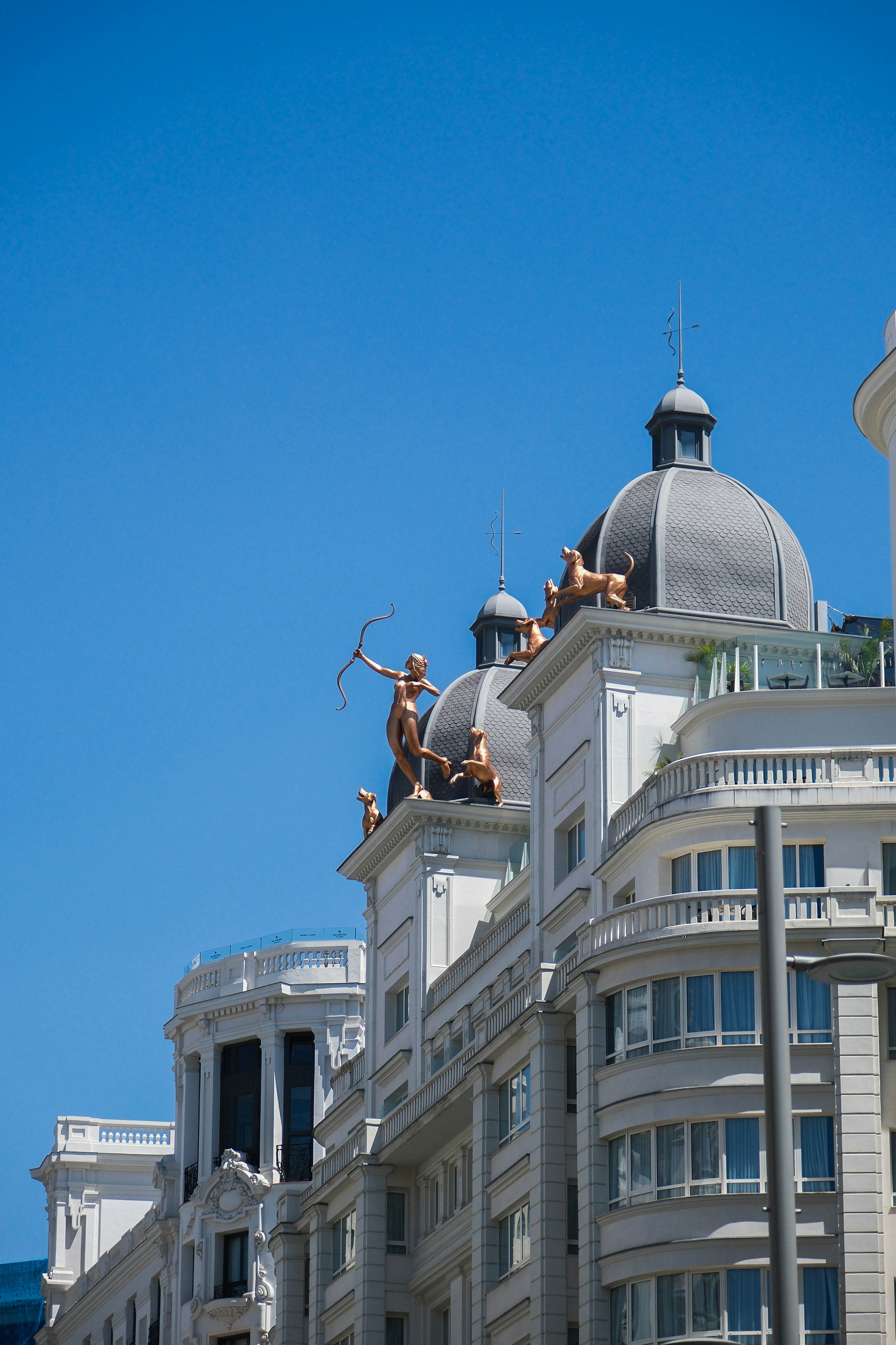 Sculptures of archers adorn the rooftop of a grand building against a clear blue sky.