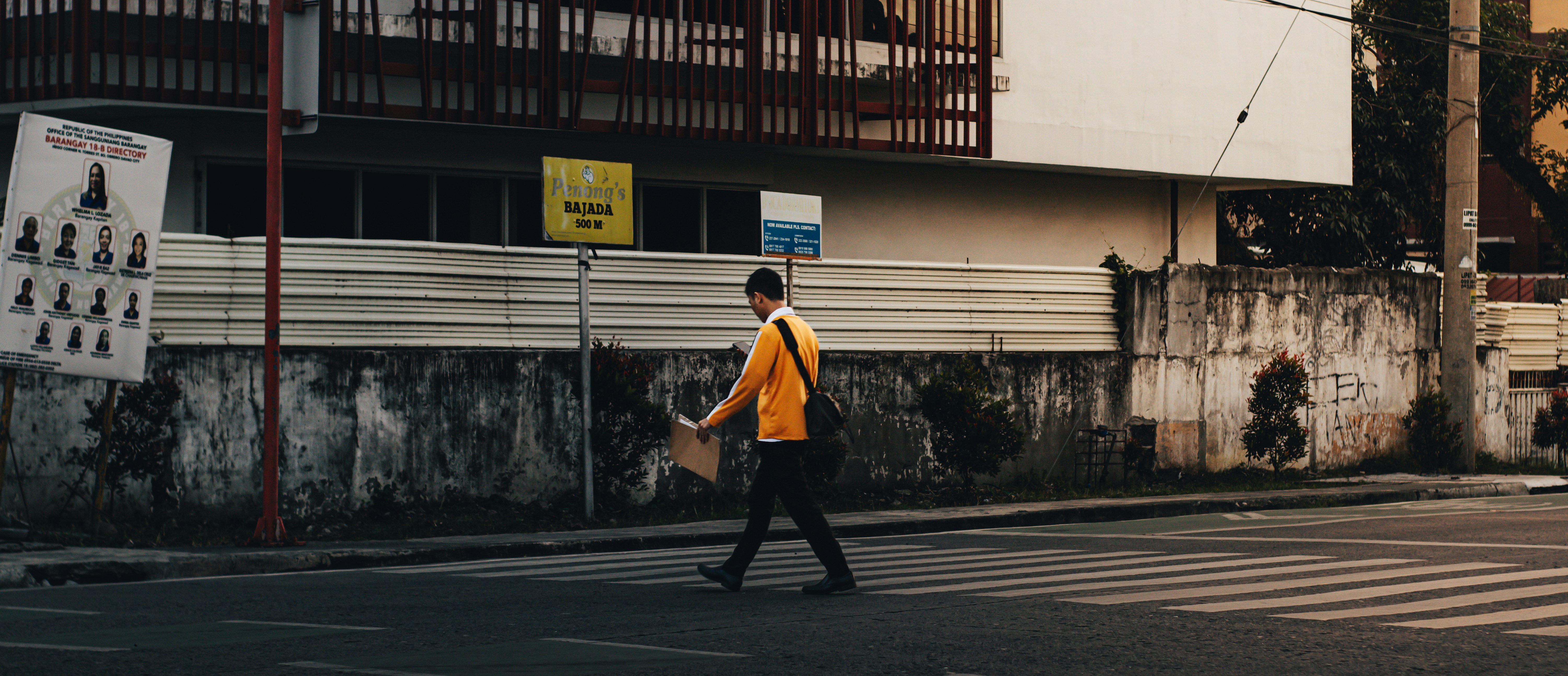 A student walks along the pedestrian lane, trying not to be late. It’s a small moment, but someone’s simple help gives them just enough time. In their own quiet way, they’re the reason our future keeps moving forward. | A man walks across the street.