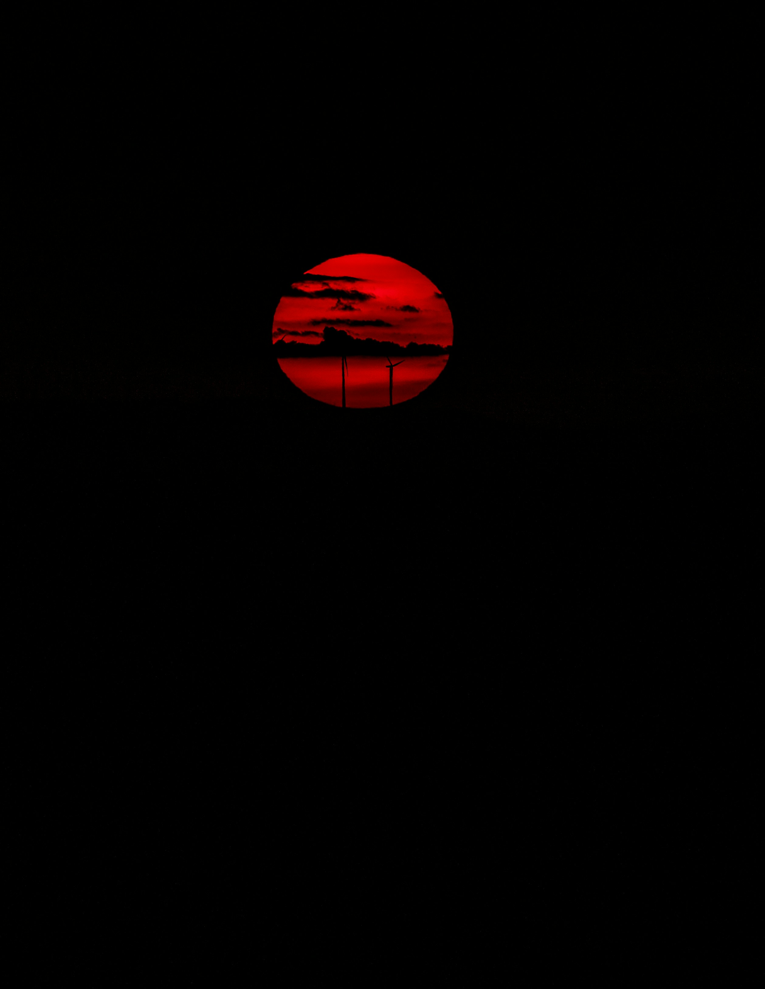 A red sun sets silhouetted by dark clouds.