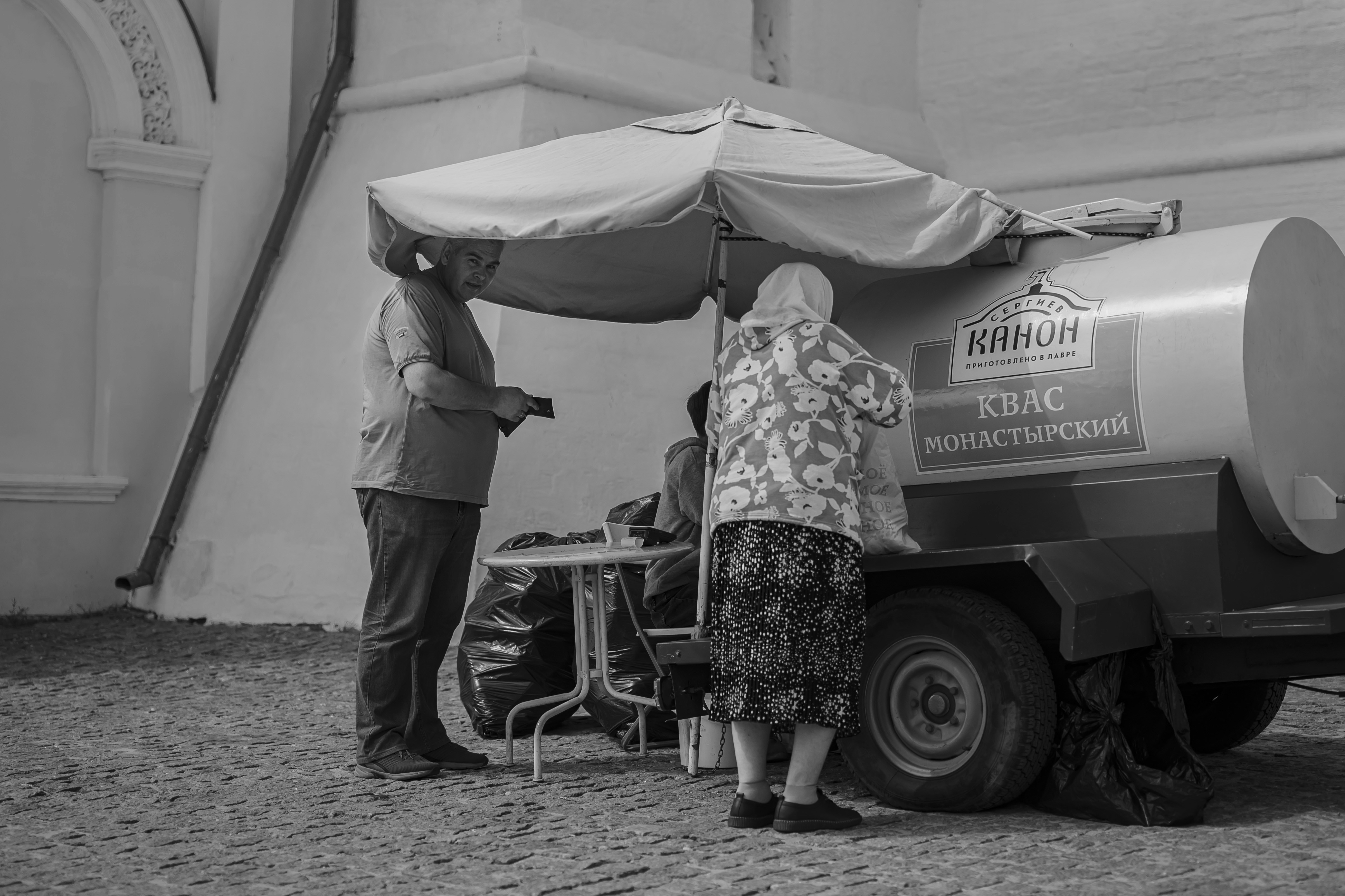 People are queuing for kvass at a retail outlet in the form of a mobile barrel. | People buy drinks from a kiosk.
