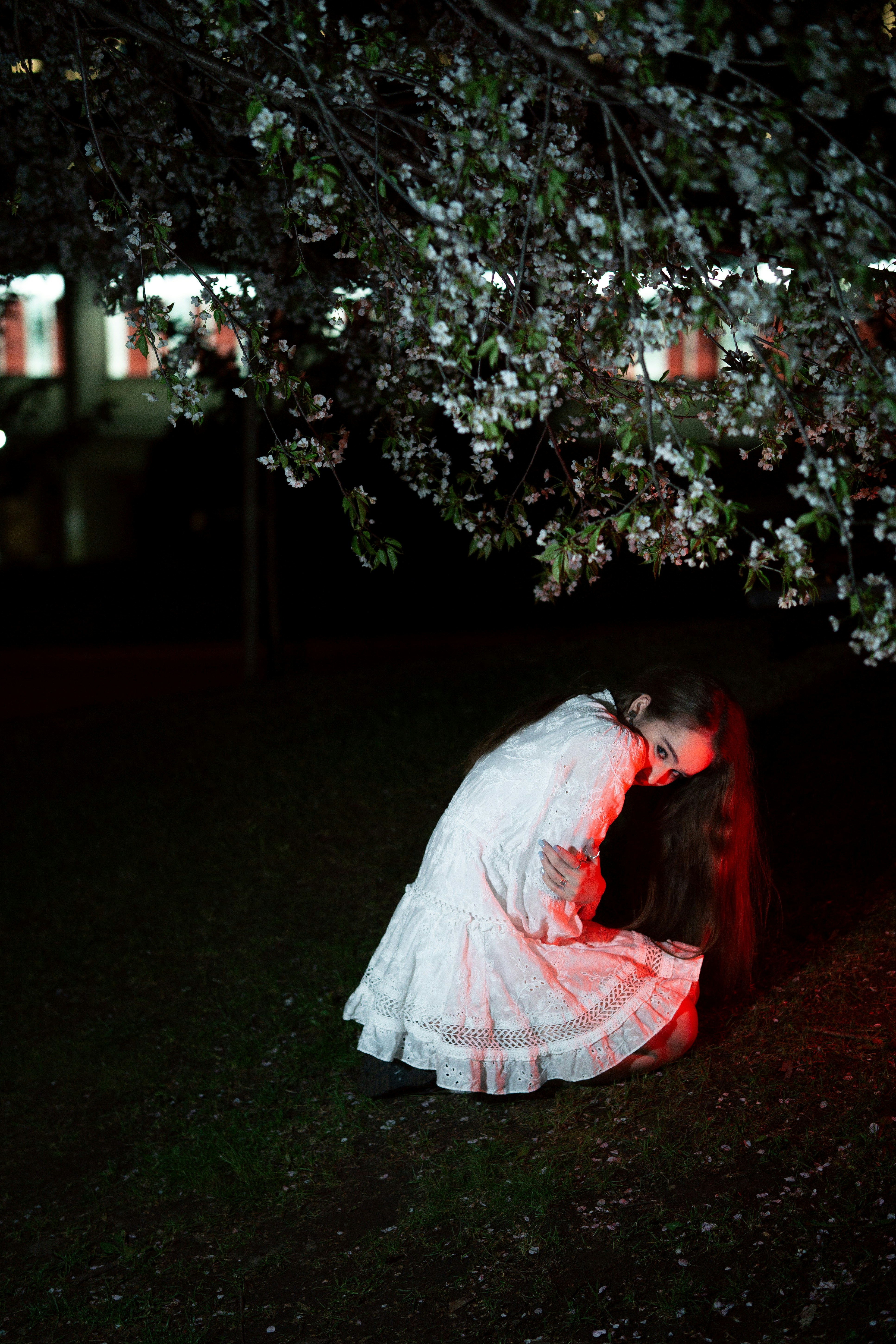 Night portrait in red light | A woman kneels in the dark under a blossoming tree.