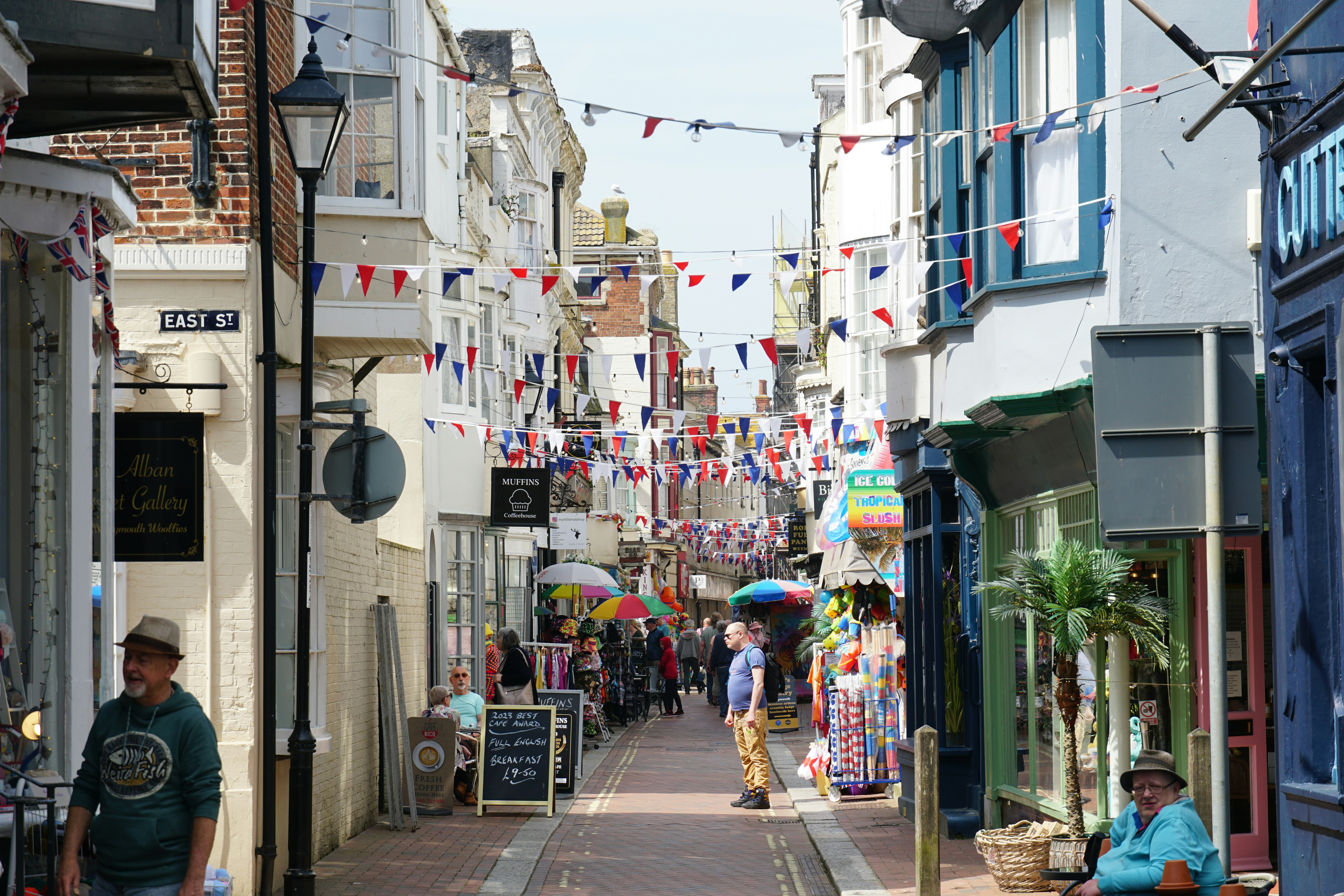 A narrow street is lined with shops and flags.
