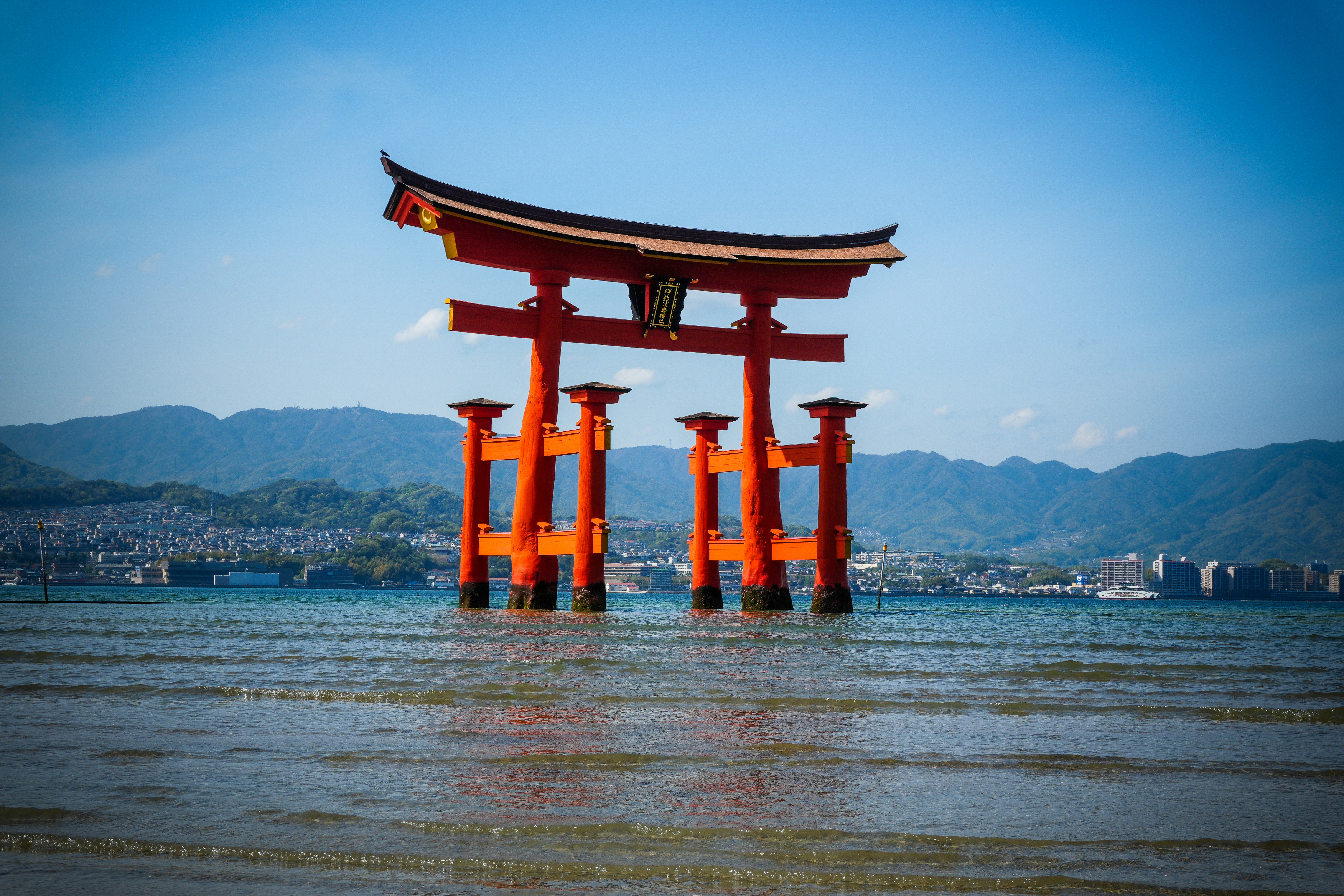 Iconic red torii gate standing majestically in shallow waters, framed by mountains in the background. The scene evokes a sense of peace and cultural significance.