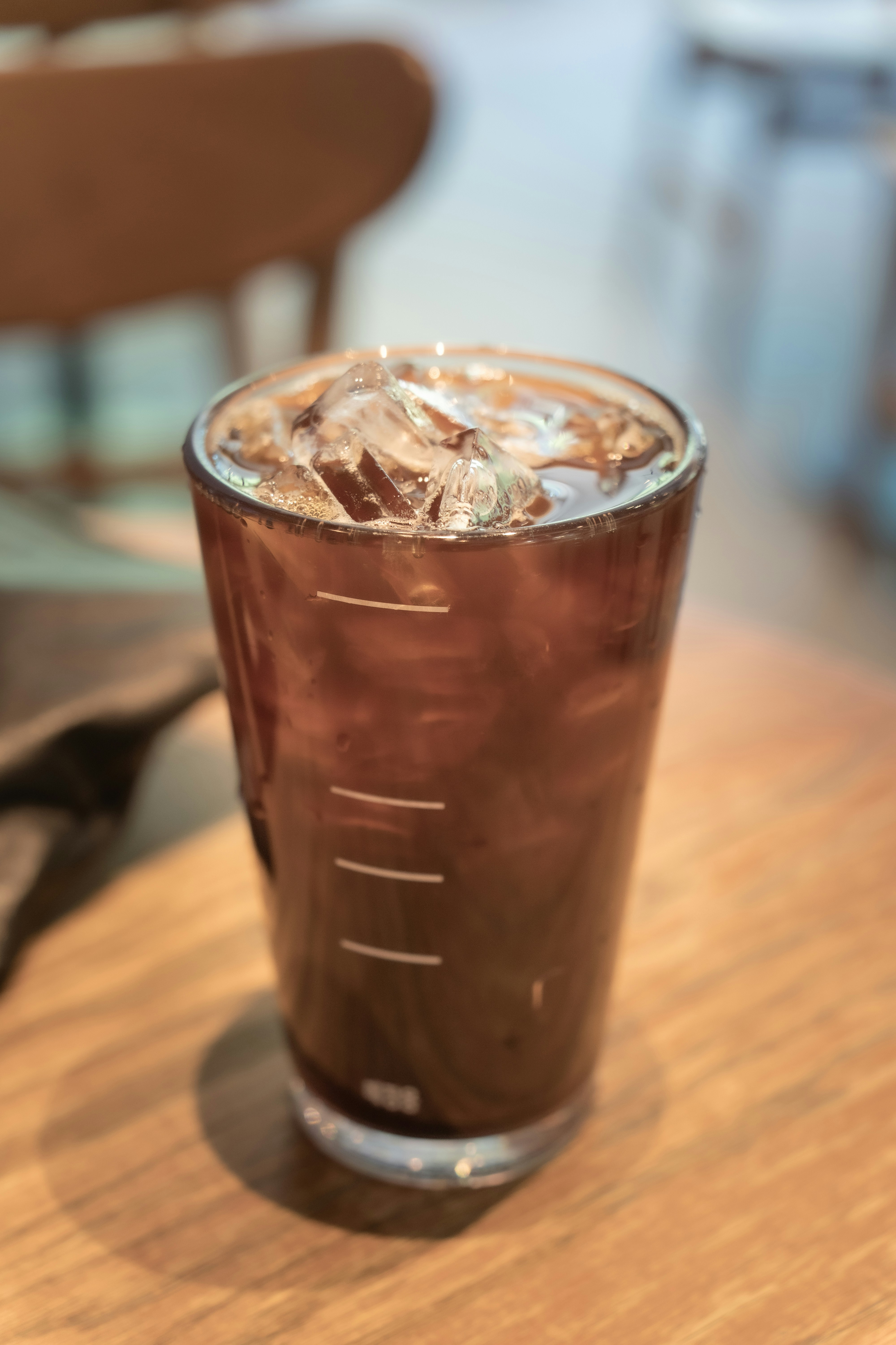 Glass filled with iced beverage, showcasing ice cubes and a rich dark color, resting on a wooden table.
