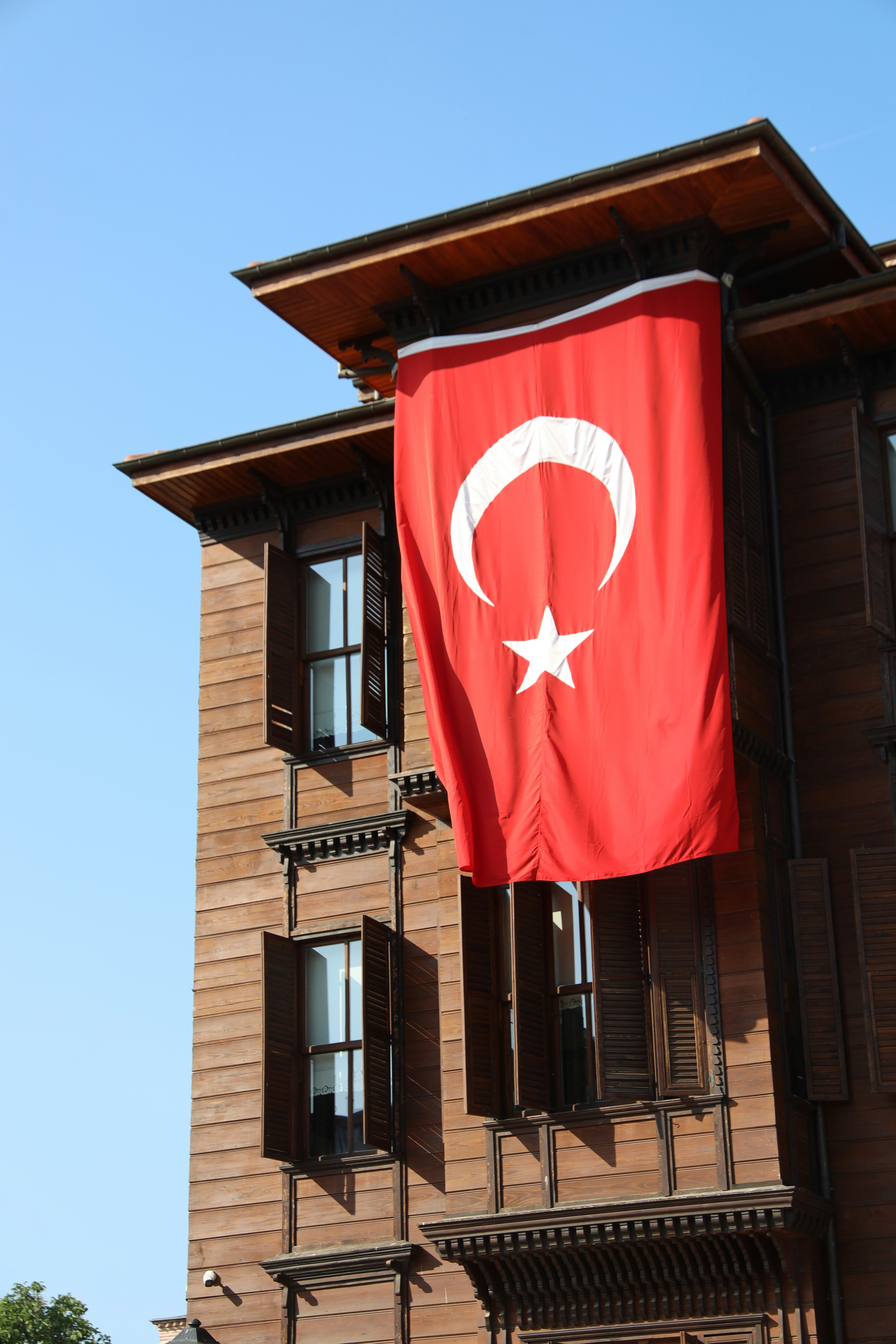 2,200 km journey across Türkiye. From the surreal landscapes of Cappadocia and its floating hot air balloons, to the spiritual silhouettes of mosques in Istanbul and the timeless beauty of the Bosphorus — a visual story of colors, contrasts, and culture. | The turkish flag hangs on a wooden building.
