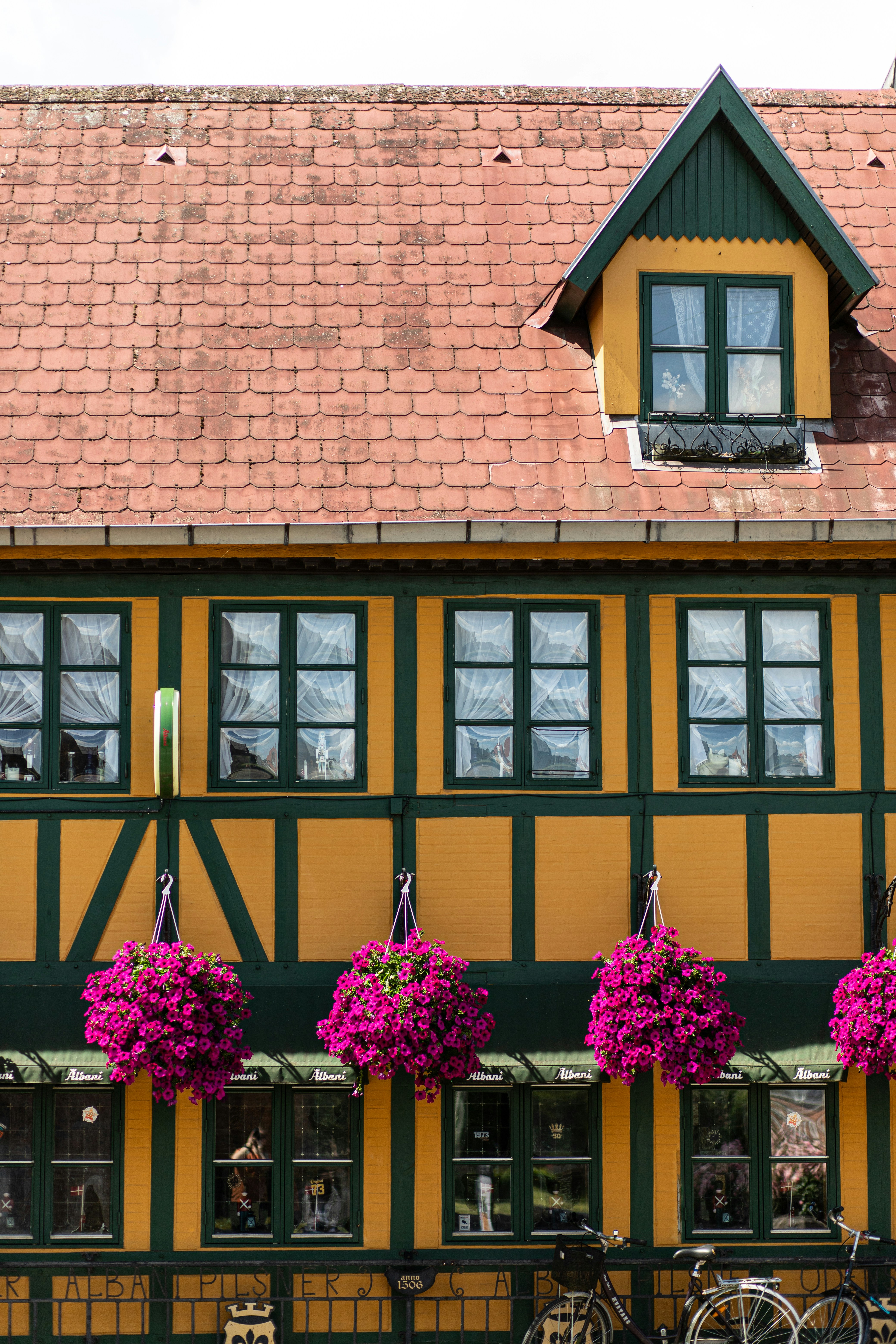Colorful cottage featuring bright yellow and green walls adorned with hanging pink flower baskets, showcasing charming architectural details.