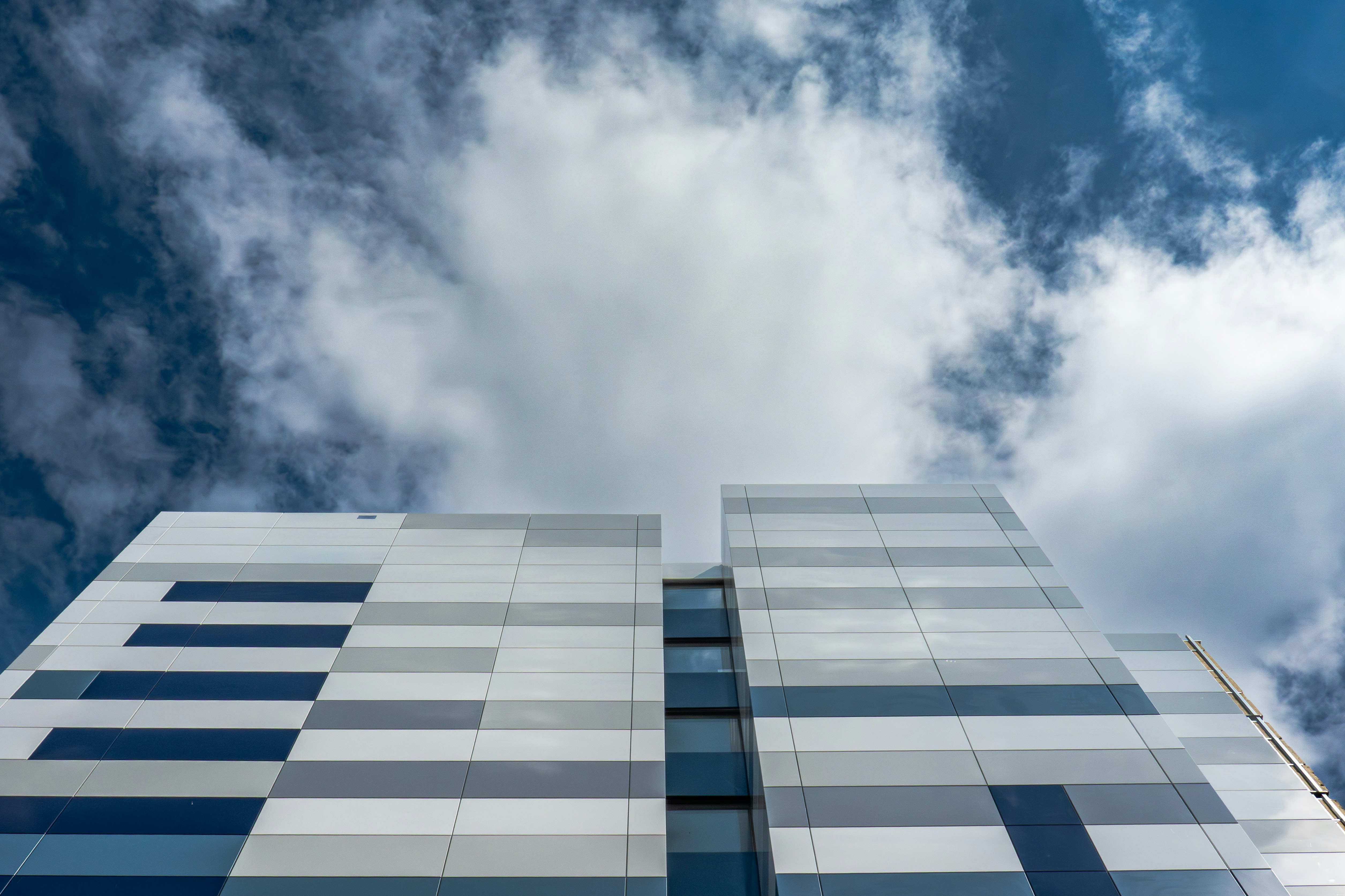 a blue and grey apartment building with vibrant skies | Building's facade against a cloudy sky.